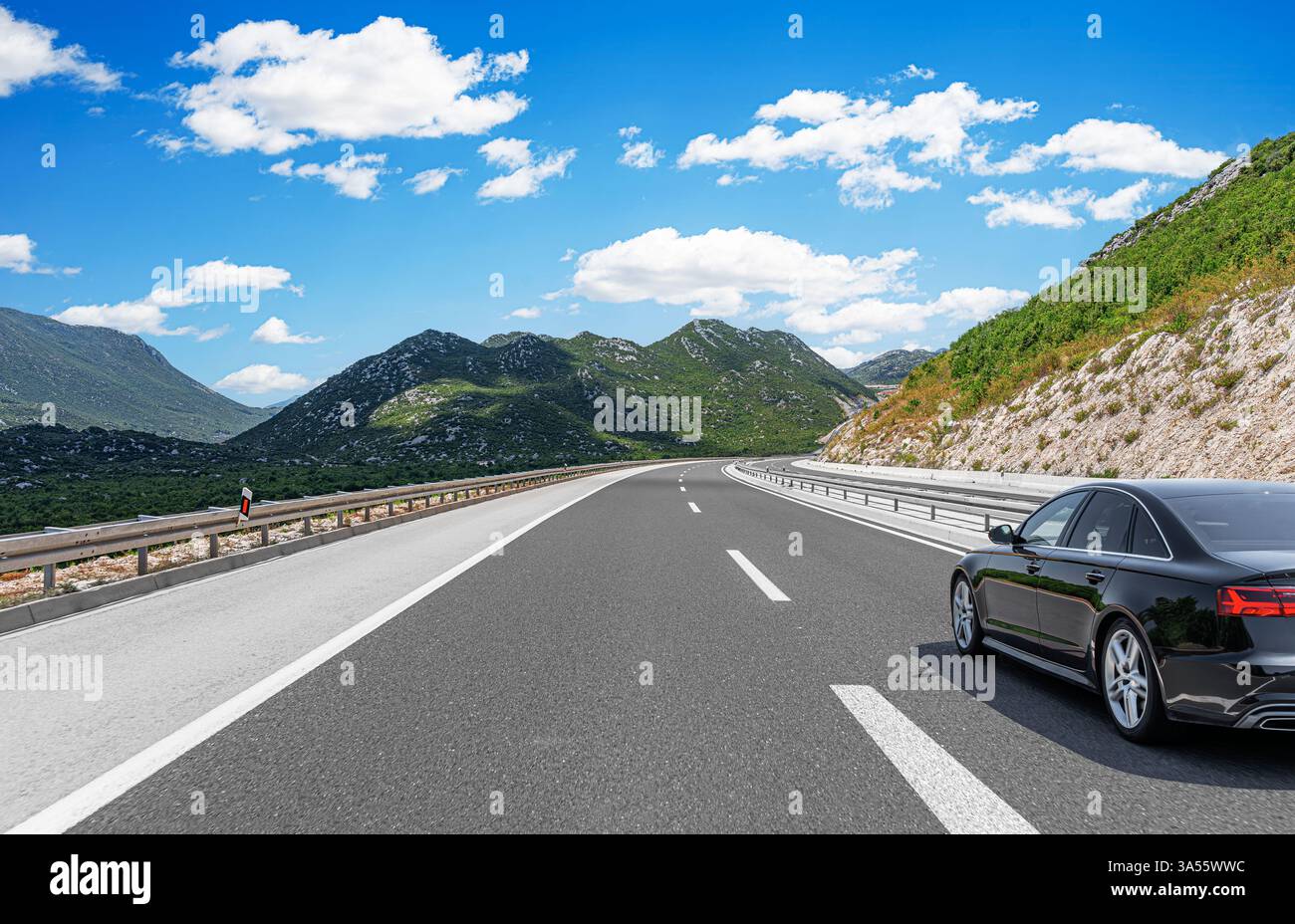 A sleek black luxury sedan cruises along a winding highway through lush ...