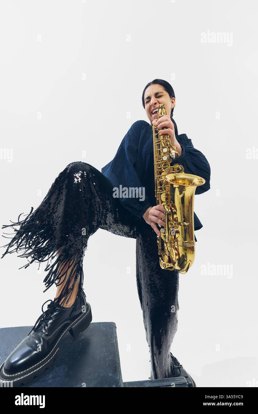 Dynamic low angle image of woman, saxophonist raising leg on platform ...