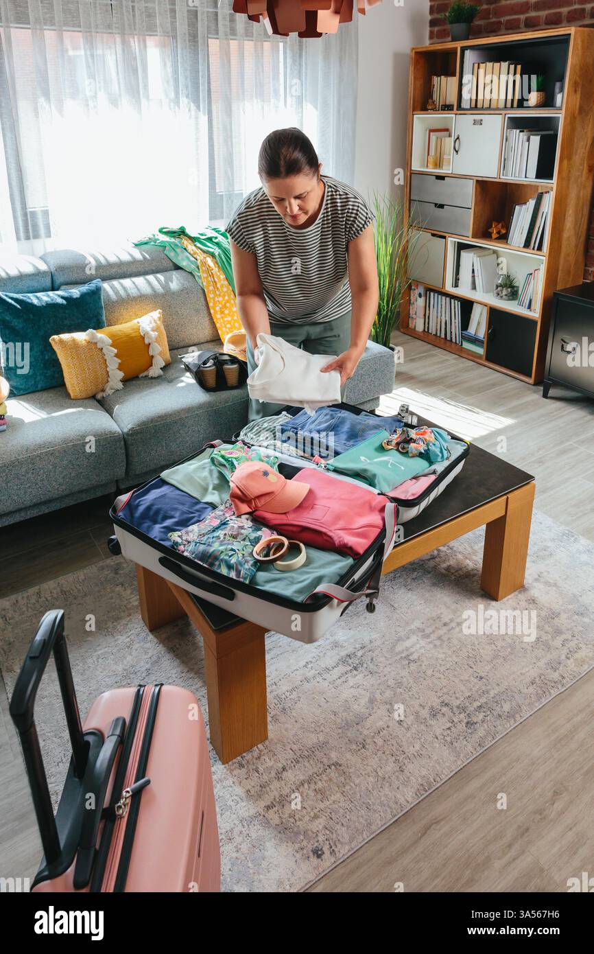 Portrait of concentrated woman packing suitcase preparing clothes for ...