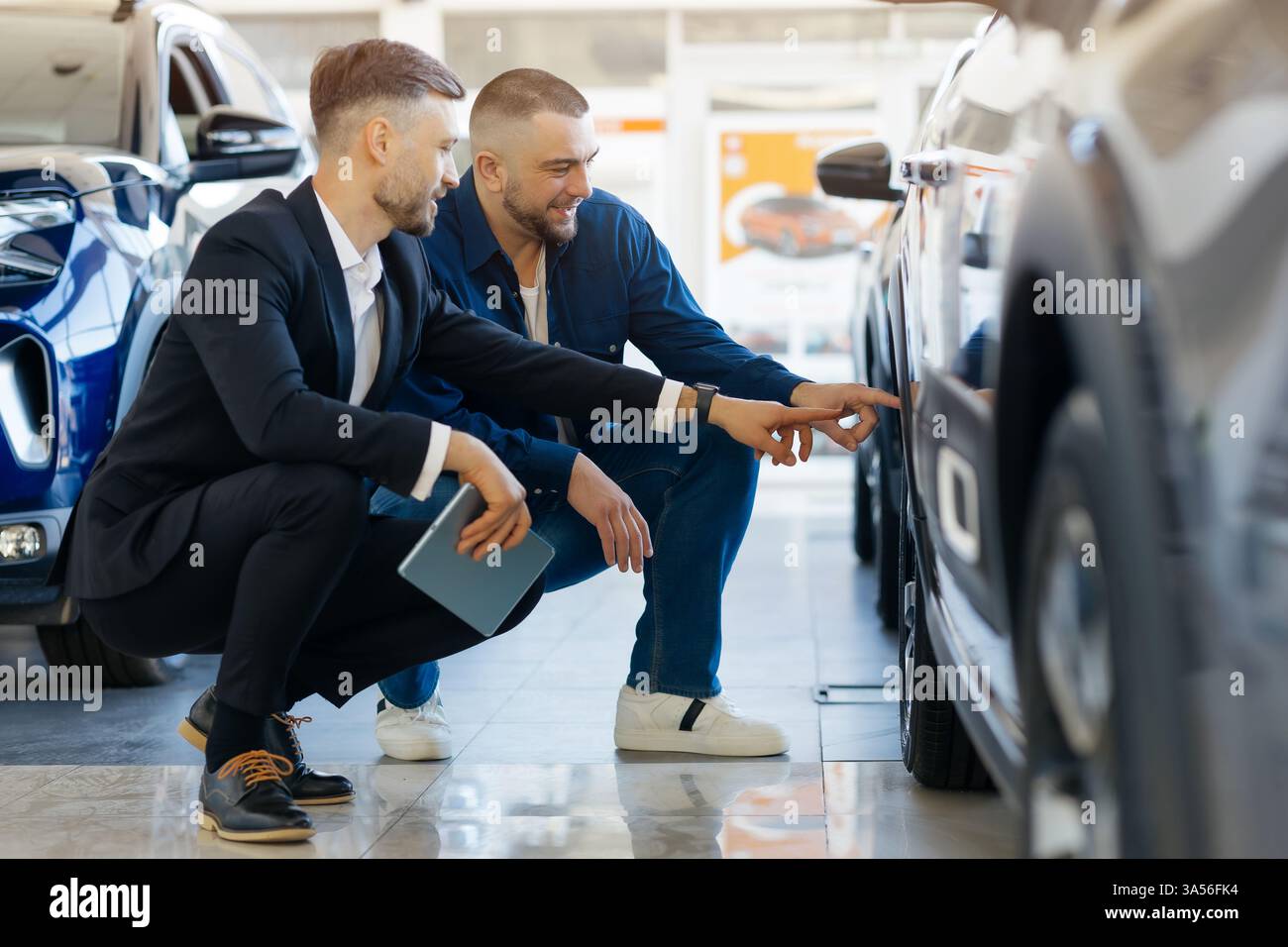Car salesman and customer crouch beside sleek vehicle in modern ...