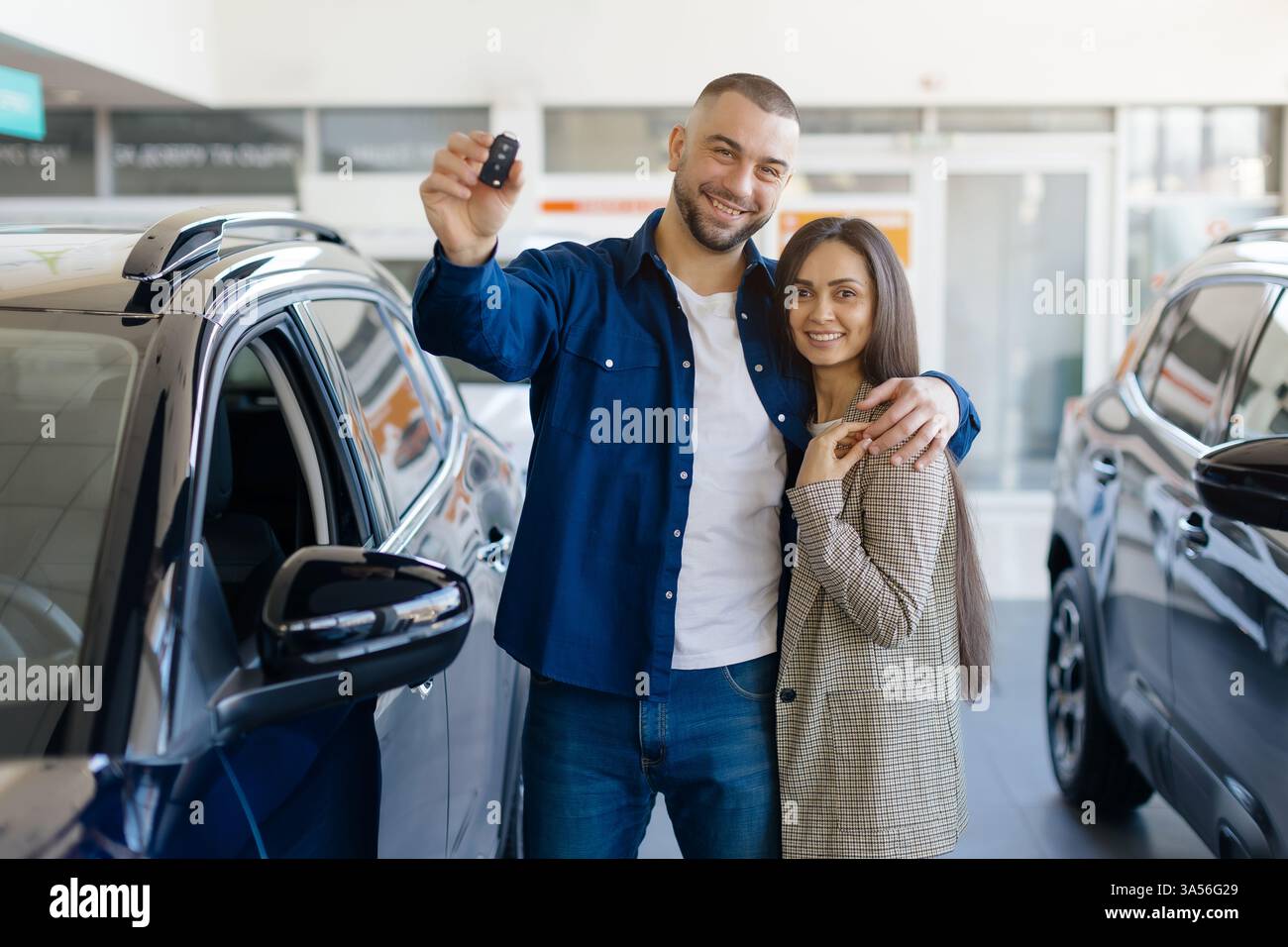 Happy Owners. Joyful Young Couple Posing With Car Keys In Dealership ...