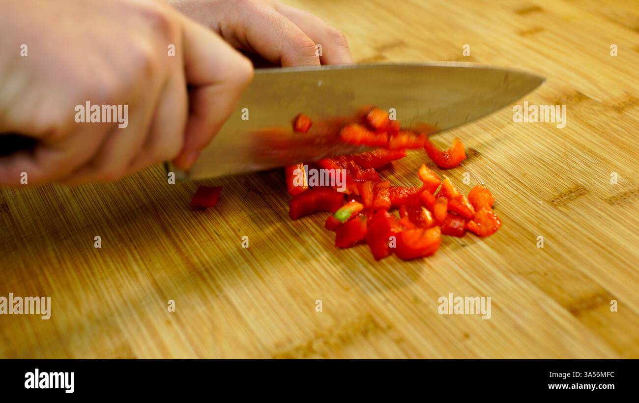 Dicing and chopping up a raw red pepper on a wooden kitchen countertop ...