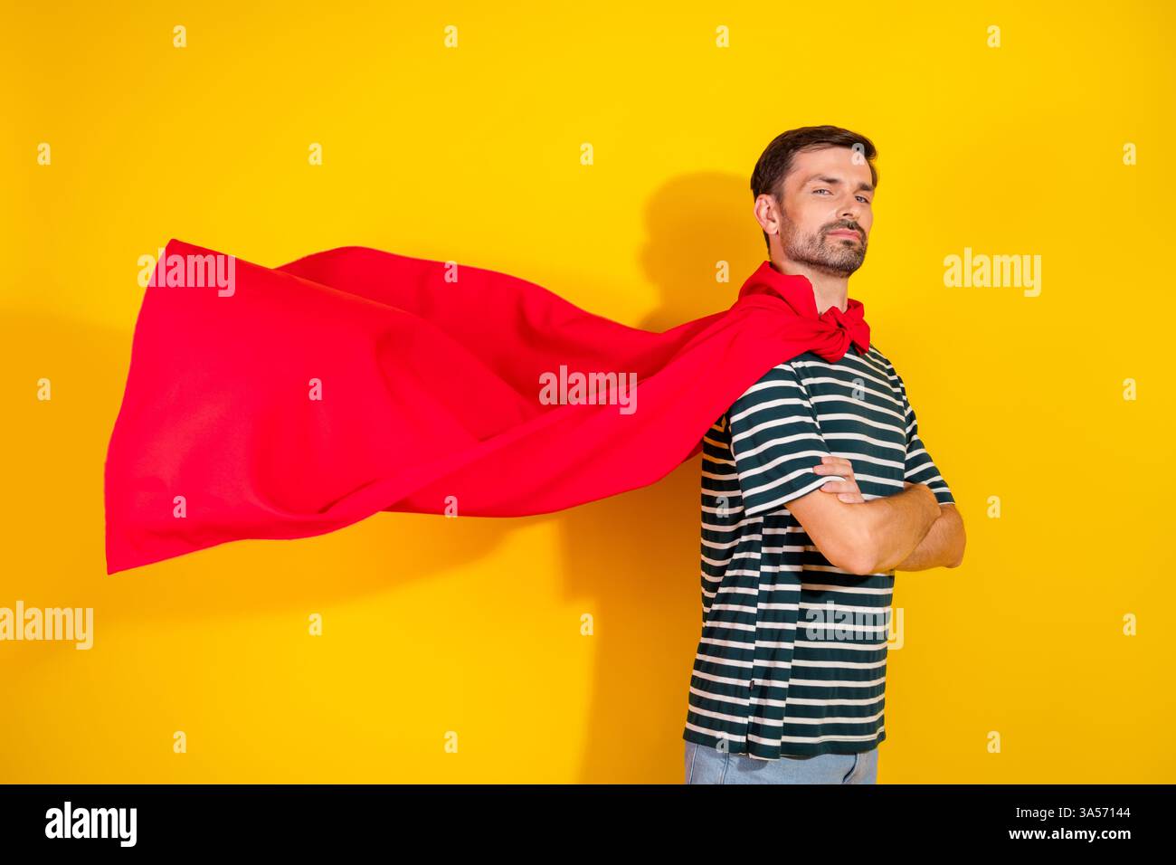 Confident young man in a red superhero cape striking a powerful pose on ...