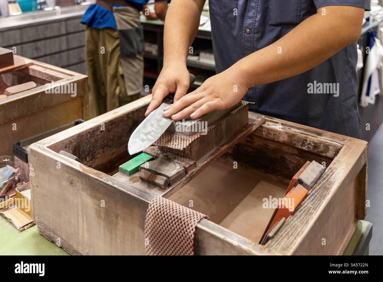 Craftsman sharpens a handmade kitchen knife using a whetstone at a ...