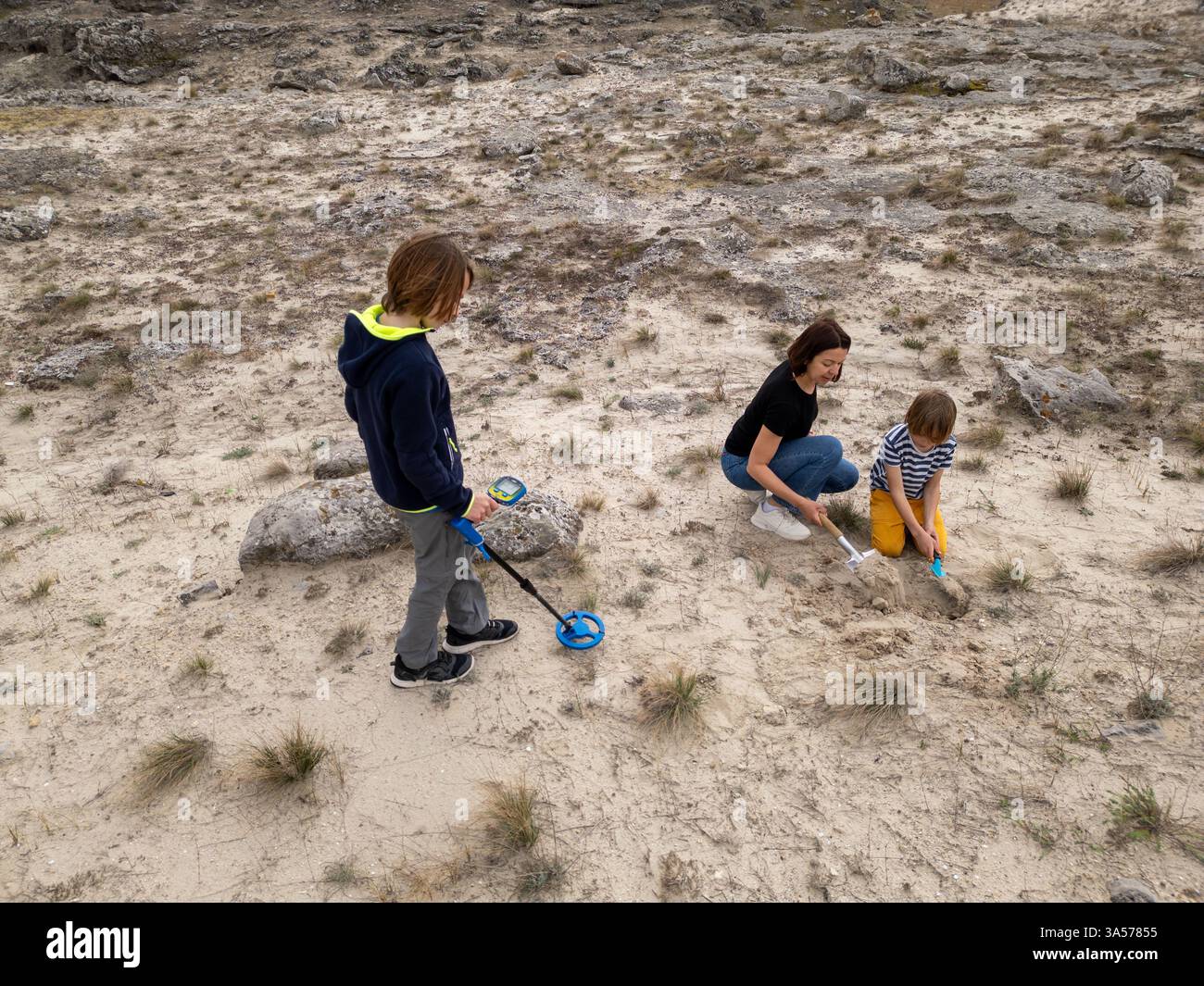 A mother and her two sons searching for treasures in a sandy outdoor ...