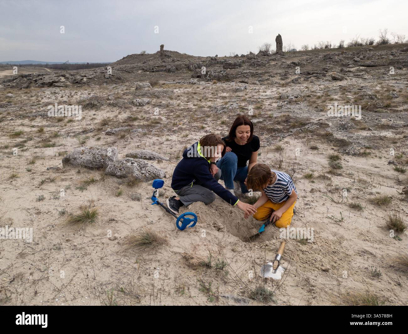 A mother and her two sons searching for treasures in a sandy outdoor ...
