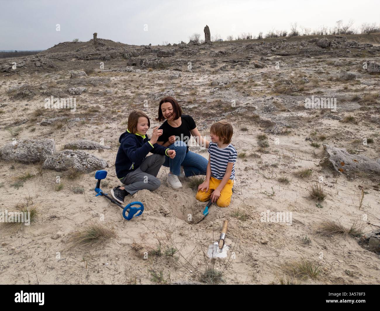 A mother and her two sons searching for treasures in a sandy outdoor ...