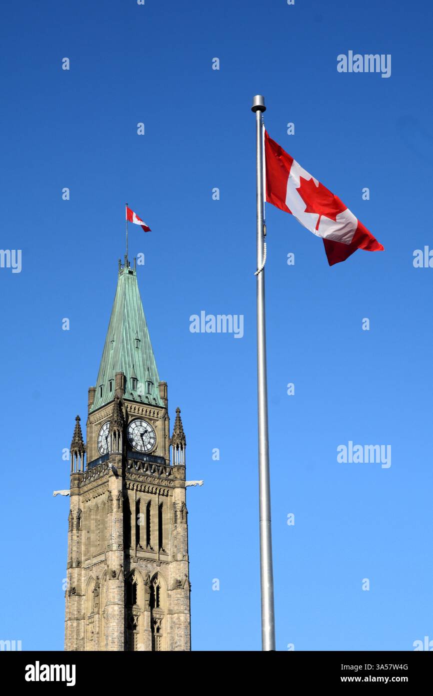 The Canadian flag flies against a blue sky with the top of the majestic Peace Tower of the ...
