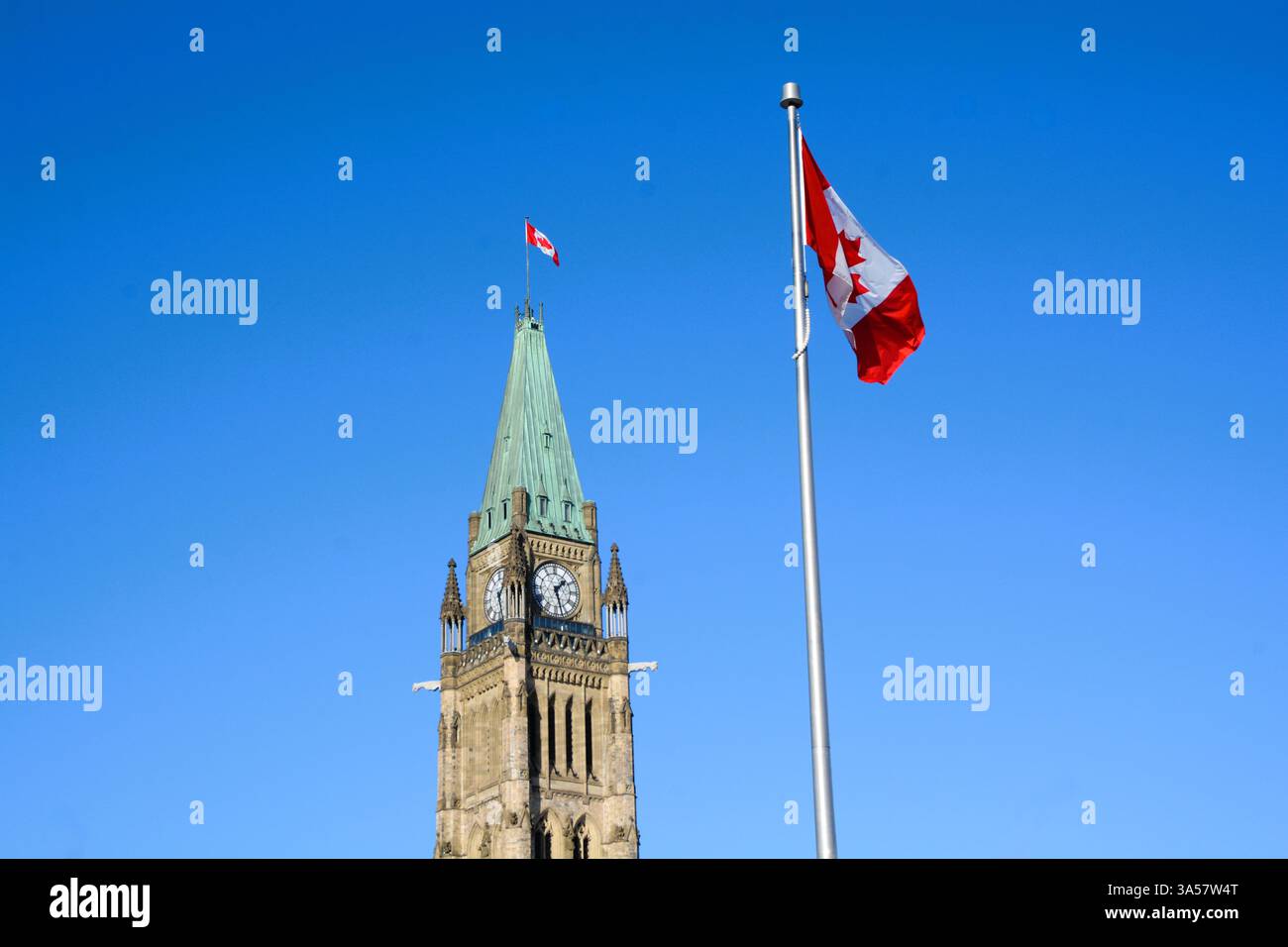 The Canadian flag flies against a blue sky with the top of the majestic Peace Tower of the ...