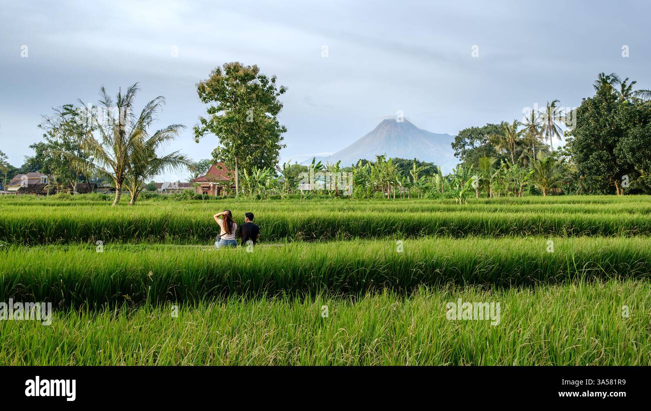 A young couple admiring mount merapi volcano from rice paddies in ...