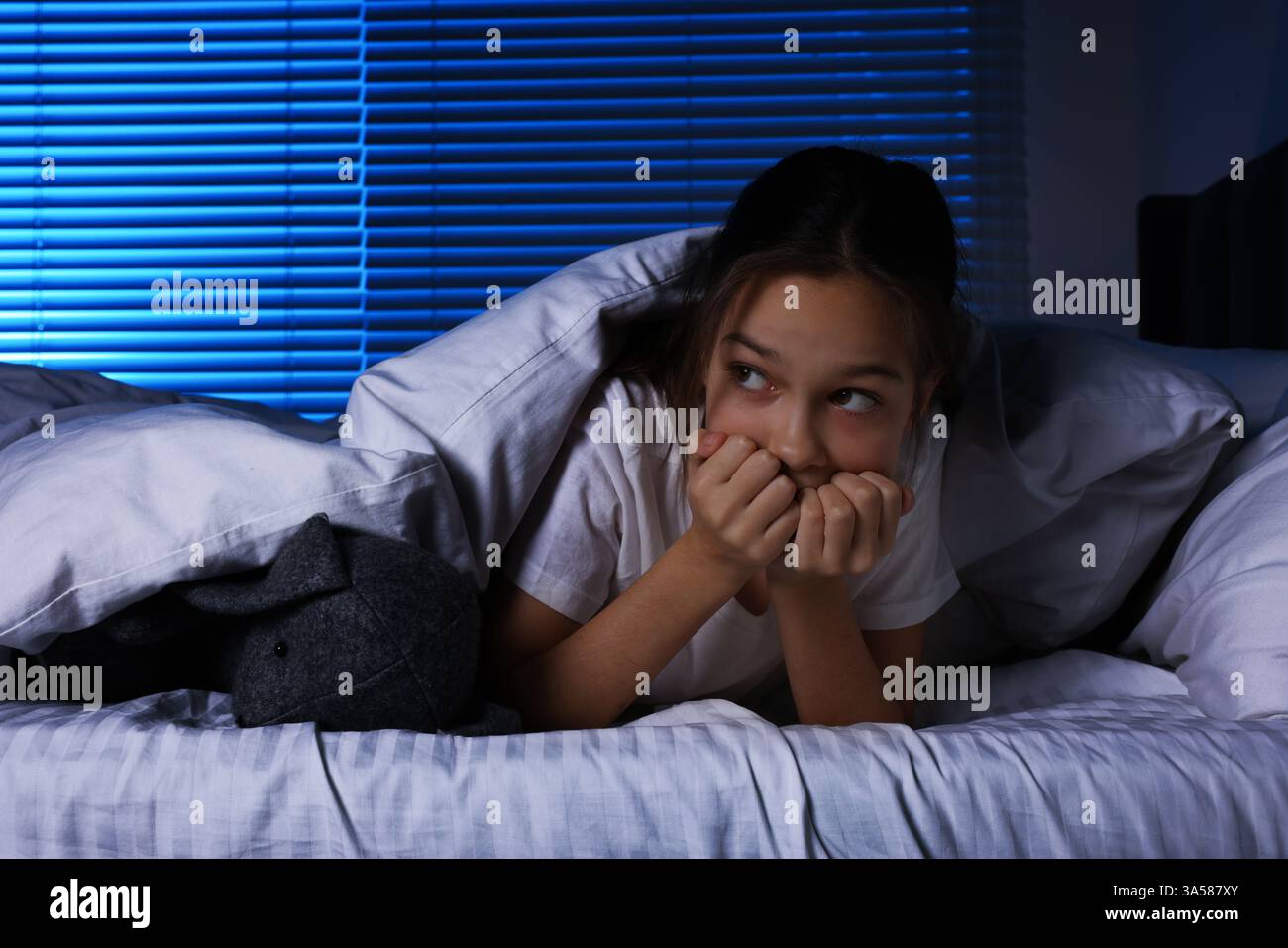 Fearful girl with toy bunny under duvet in bed at night Stock Photo - Alamy