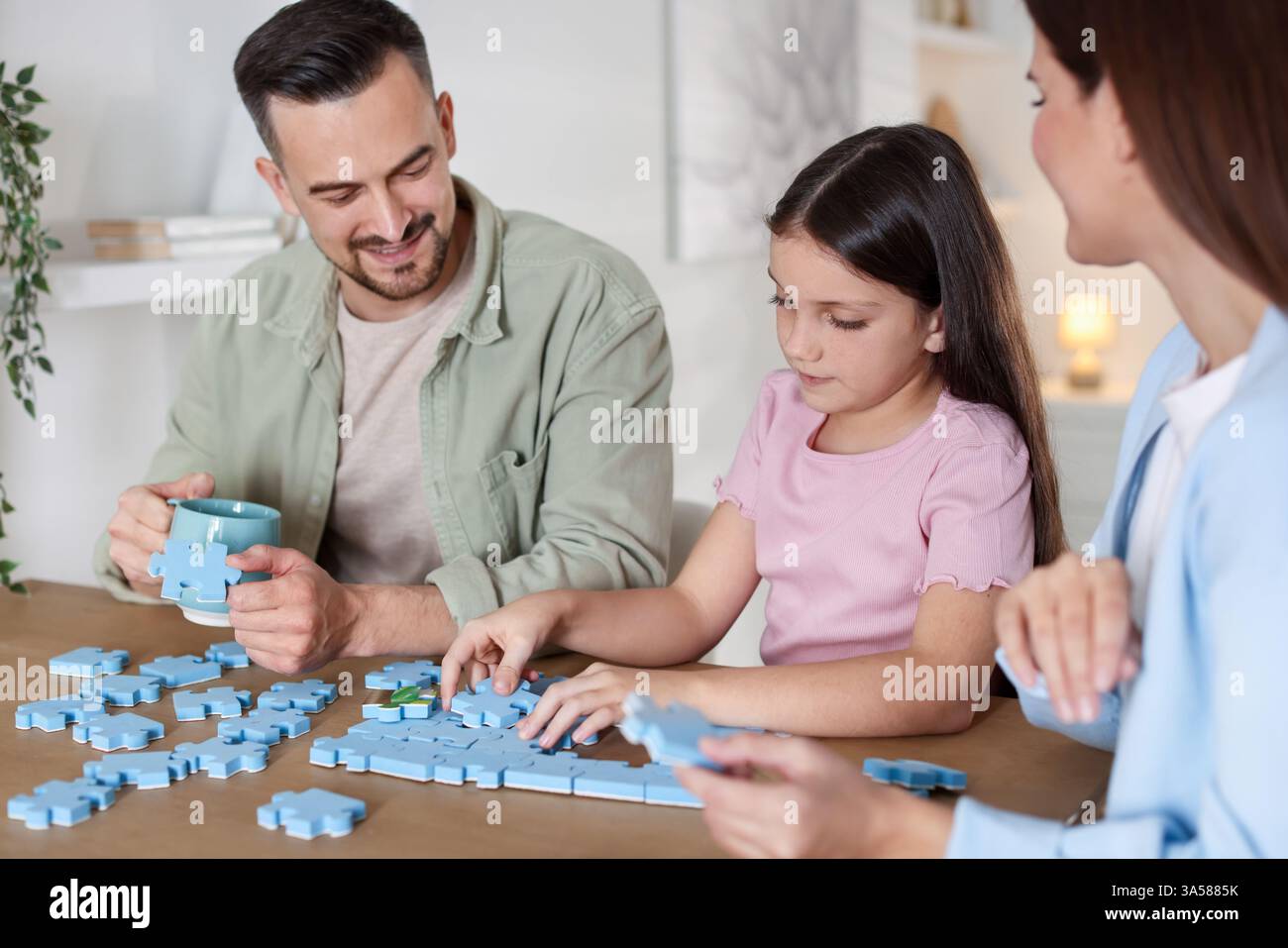 Happy parents and their daughter solving puzzle together at wooden ...