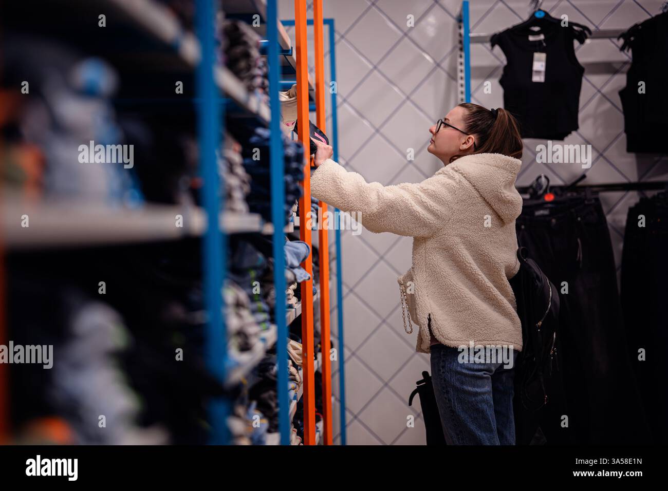 A woman in a cozy fleece jacket browses folded clothes on store shelves ...