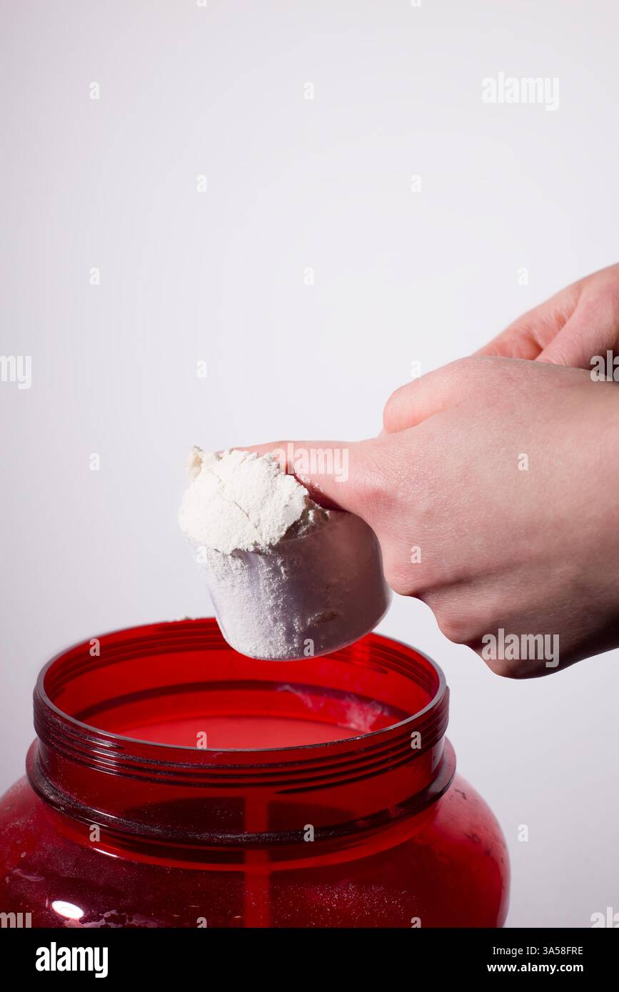 finger measuring professional protein with measuring spoon from red jar ...