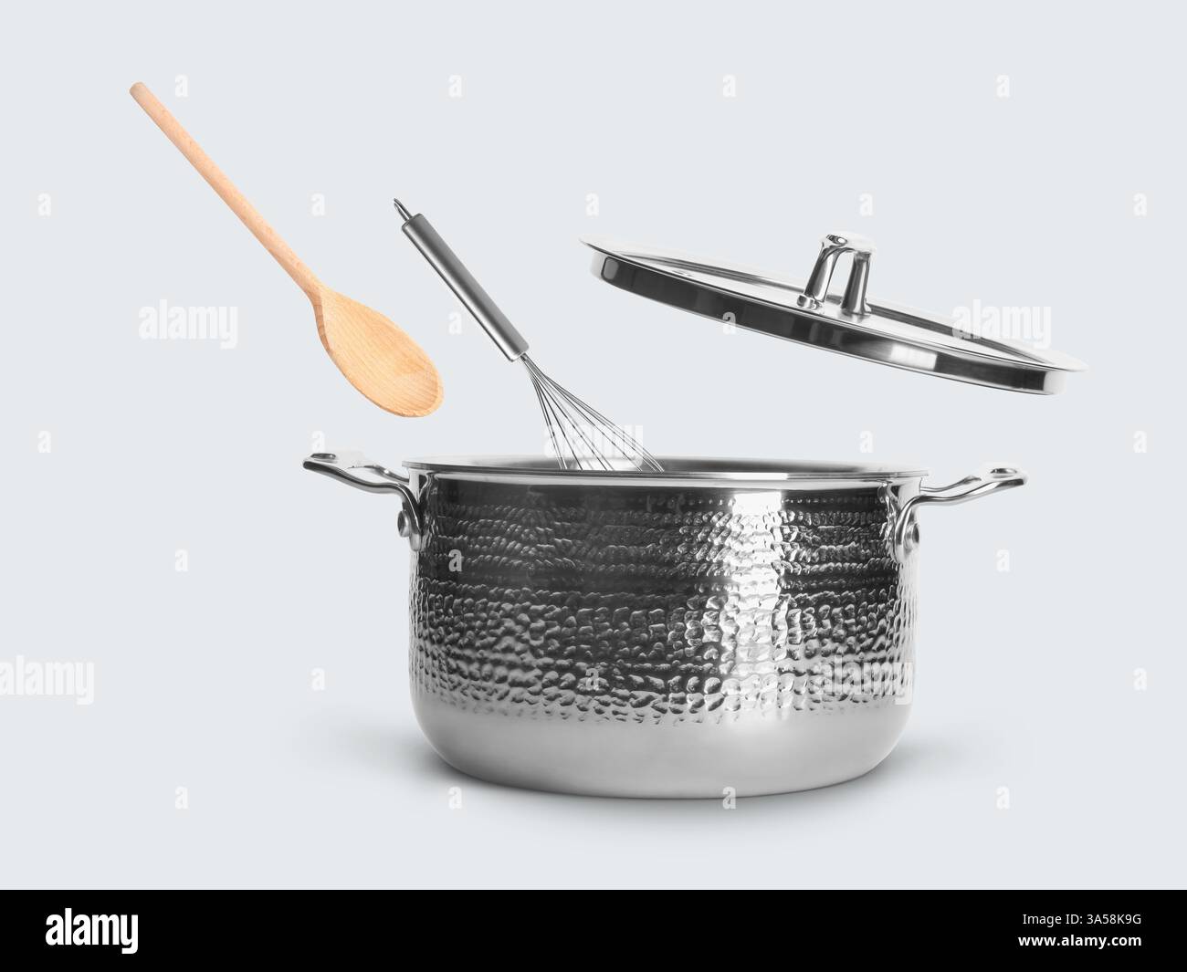 Wooden spoon and whisk in air over saucepan on white background Stock ...