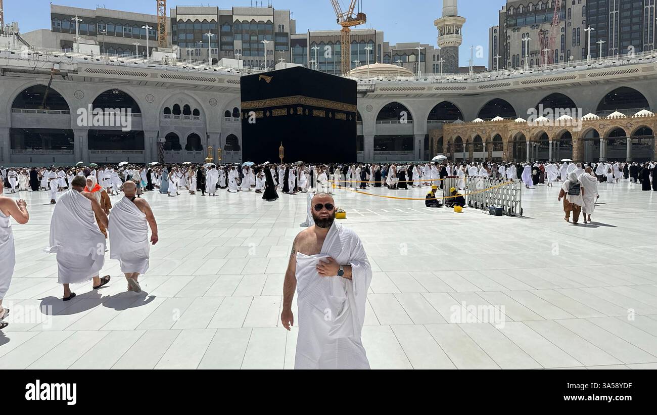 A bald man poses for a photo in front of the Kaaba at noon after ...
