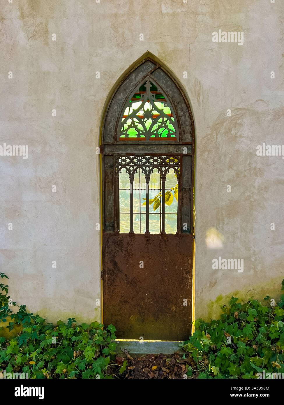 A sunlit gothic arch window door with stained glass in an old garden ...