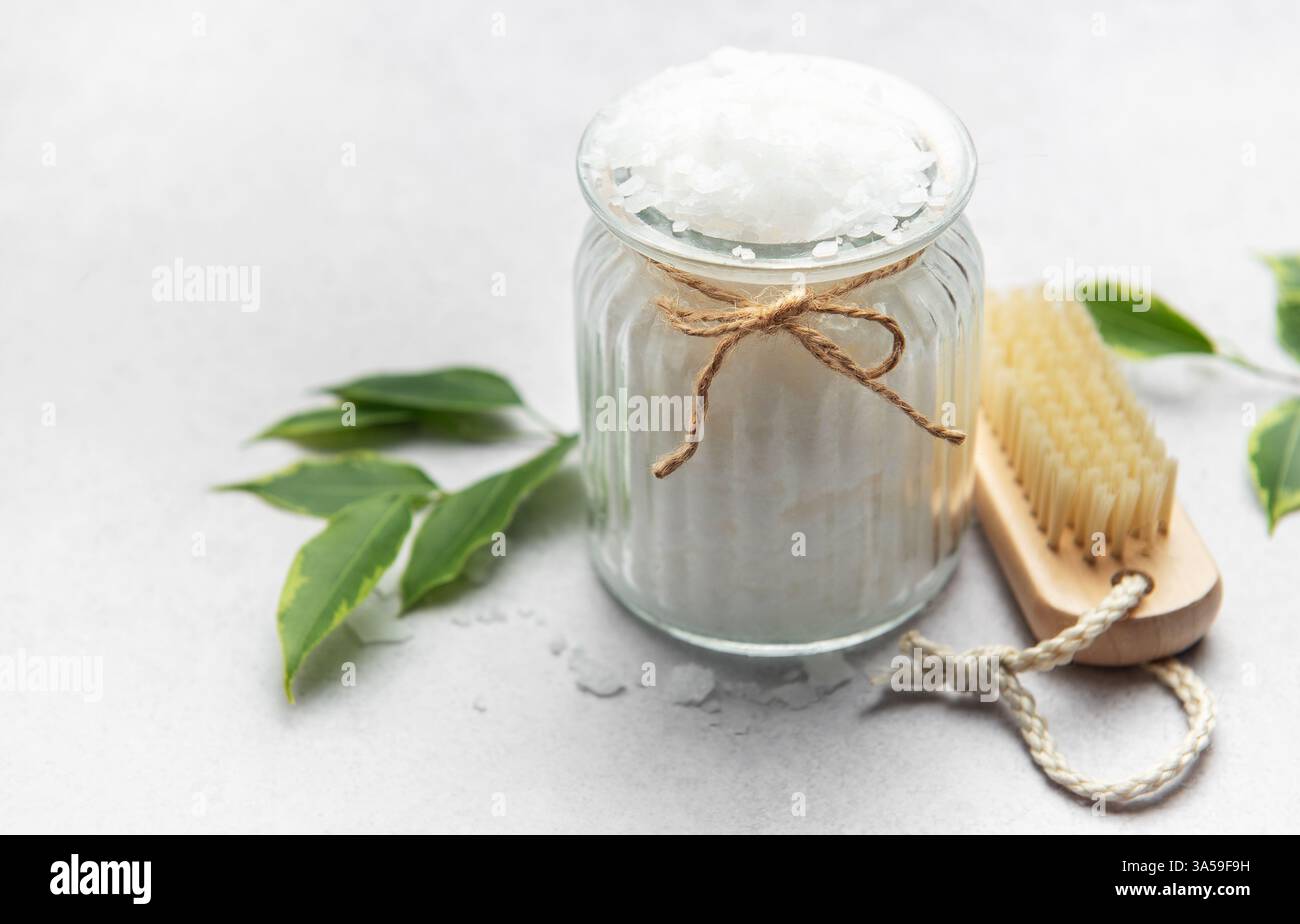 Magnesium bath flakes in glass jar, wooden brush and green leaves ...