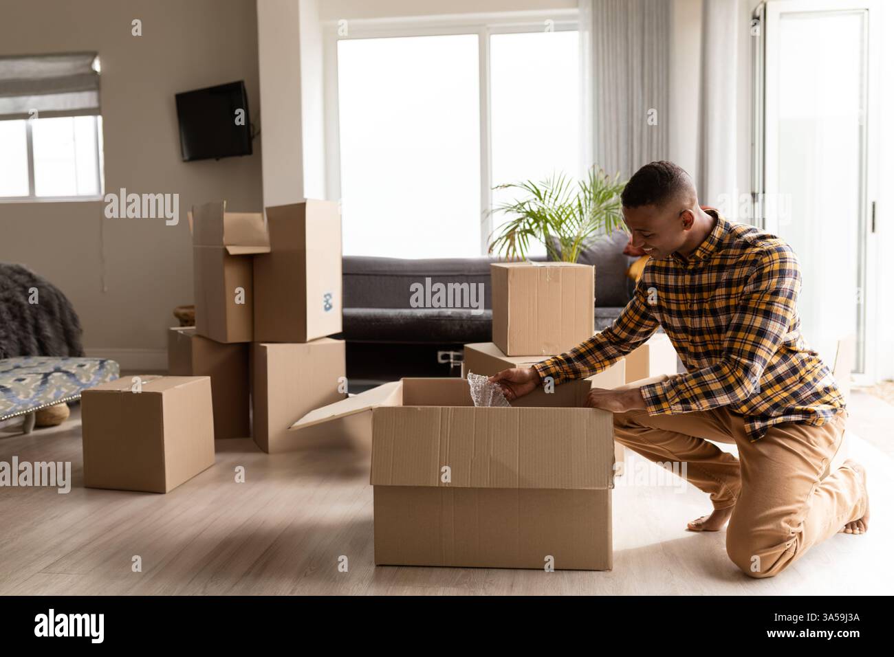 Man unpacking boxes in living room, organizing new home with care, copy ...