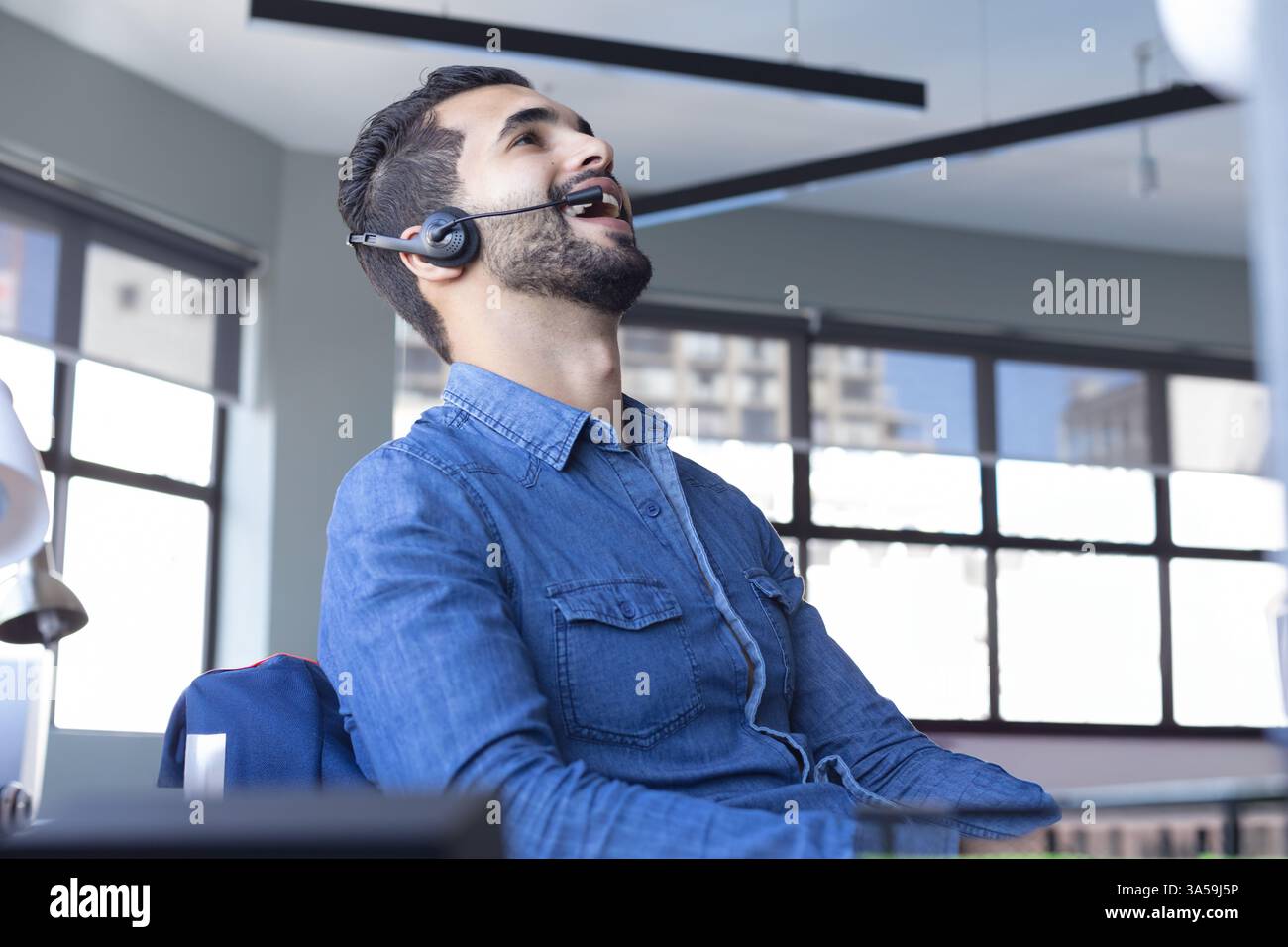 At office desk, businessman wearing headset laughing while working on ...