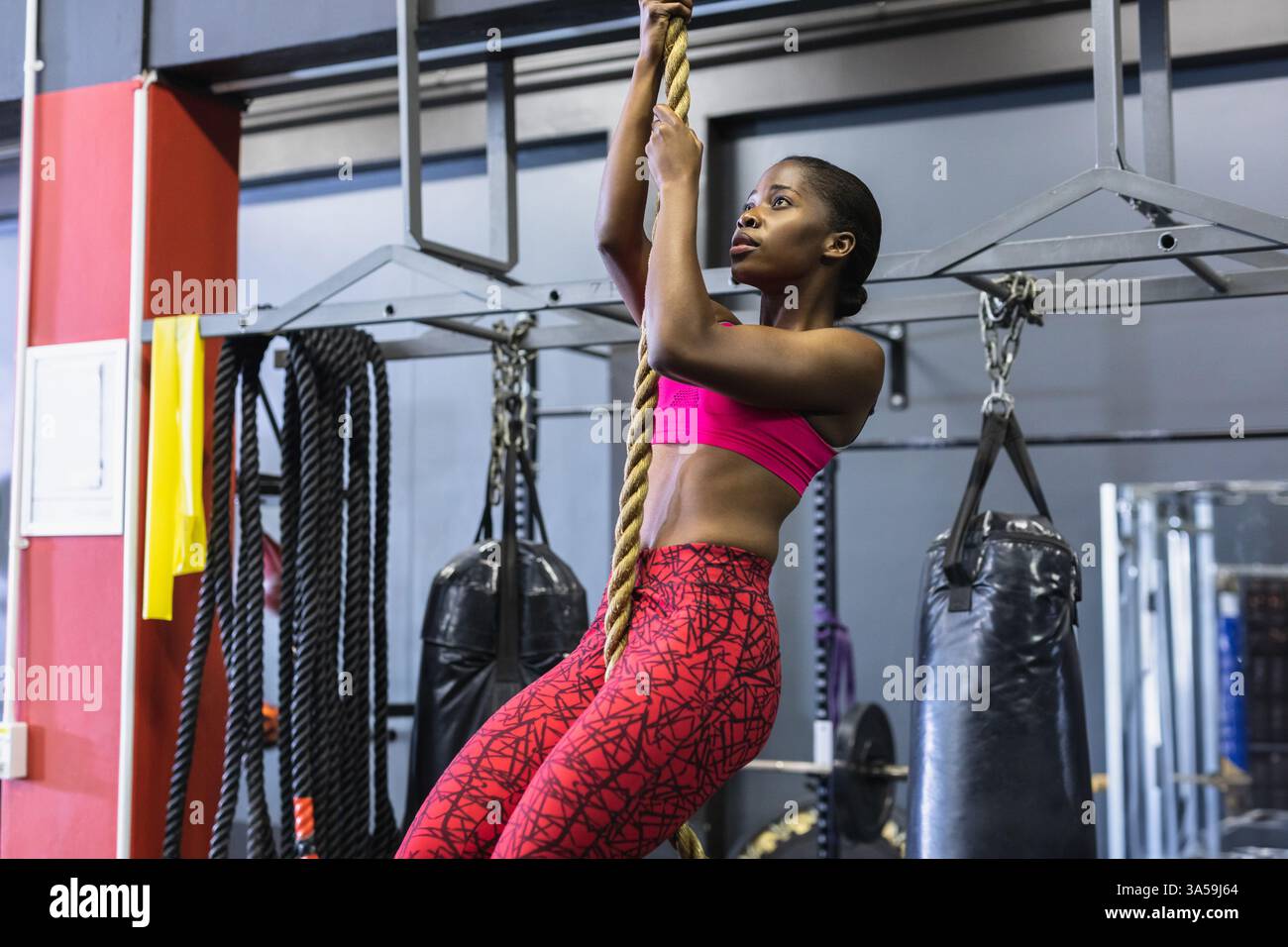 Athletic woman climbing rope in gym, focused on strength and endurance ...