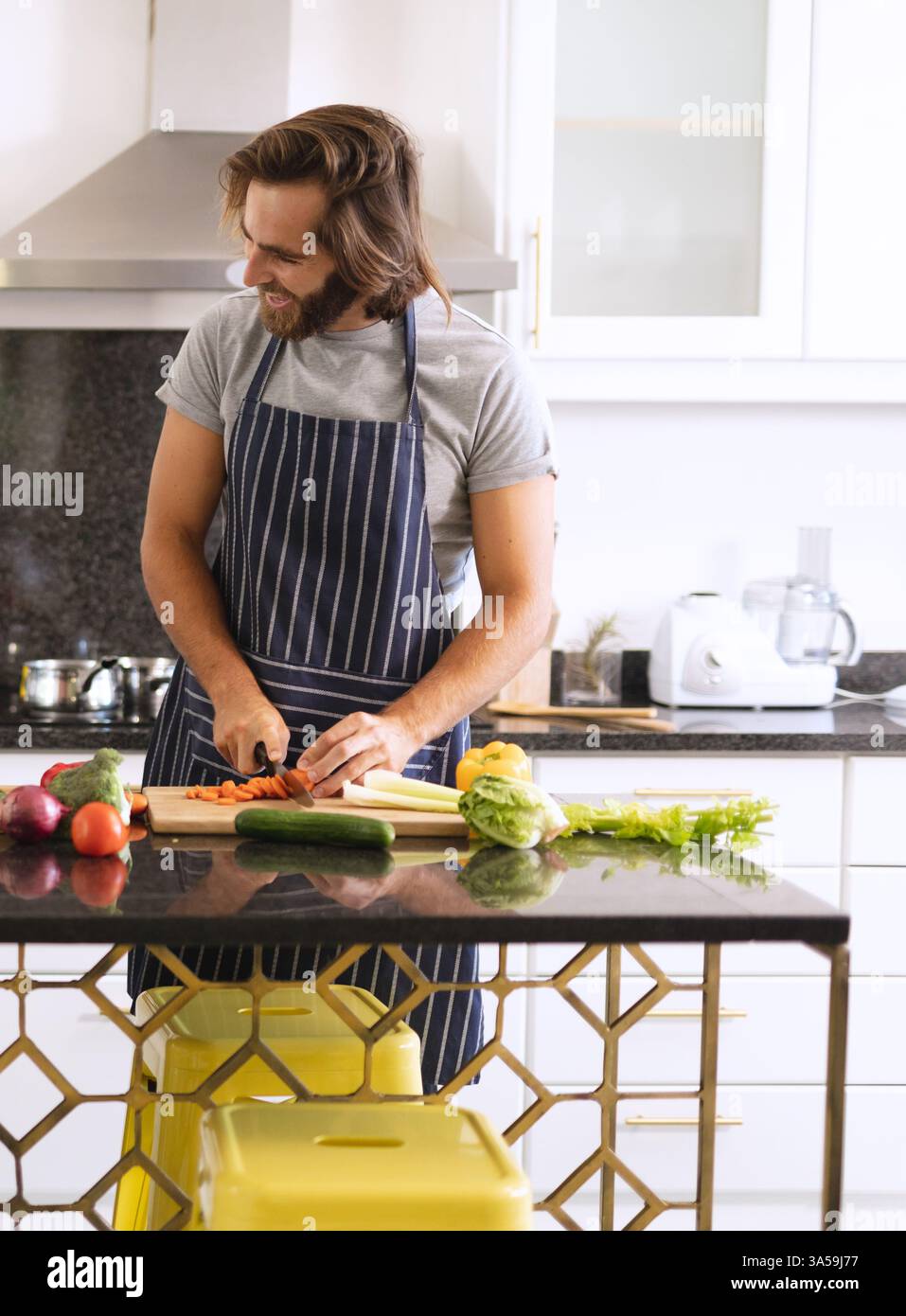Man in kitchen chopping vegetables on counter, wearing apron, smiling ...