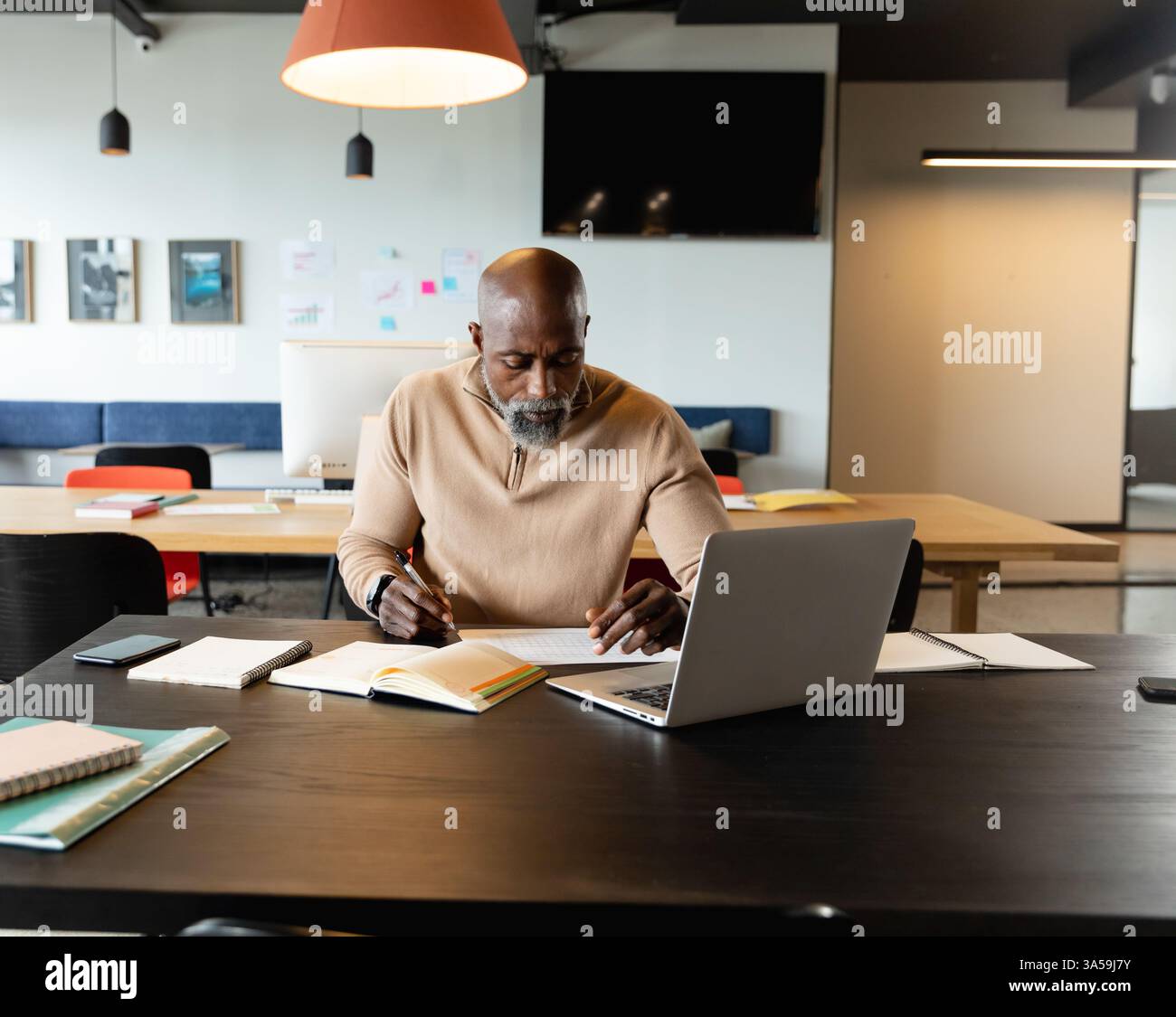 African American man working on laptop and writing notes at office desk ...