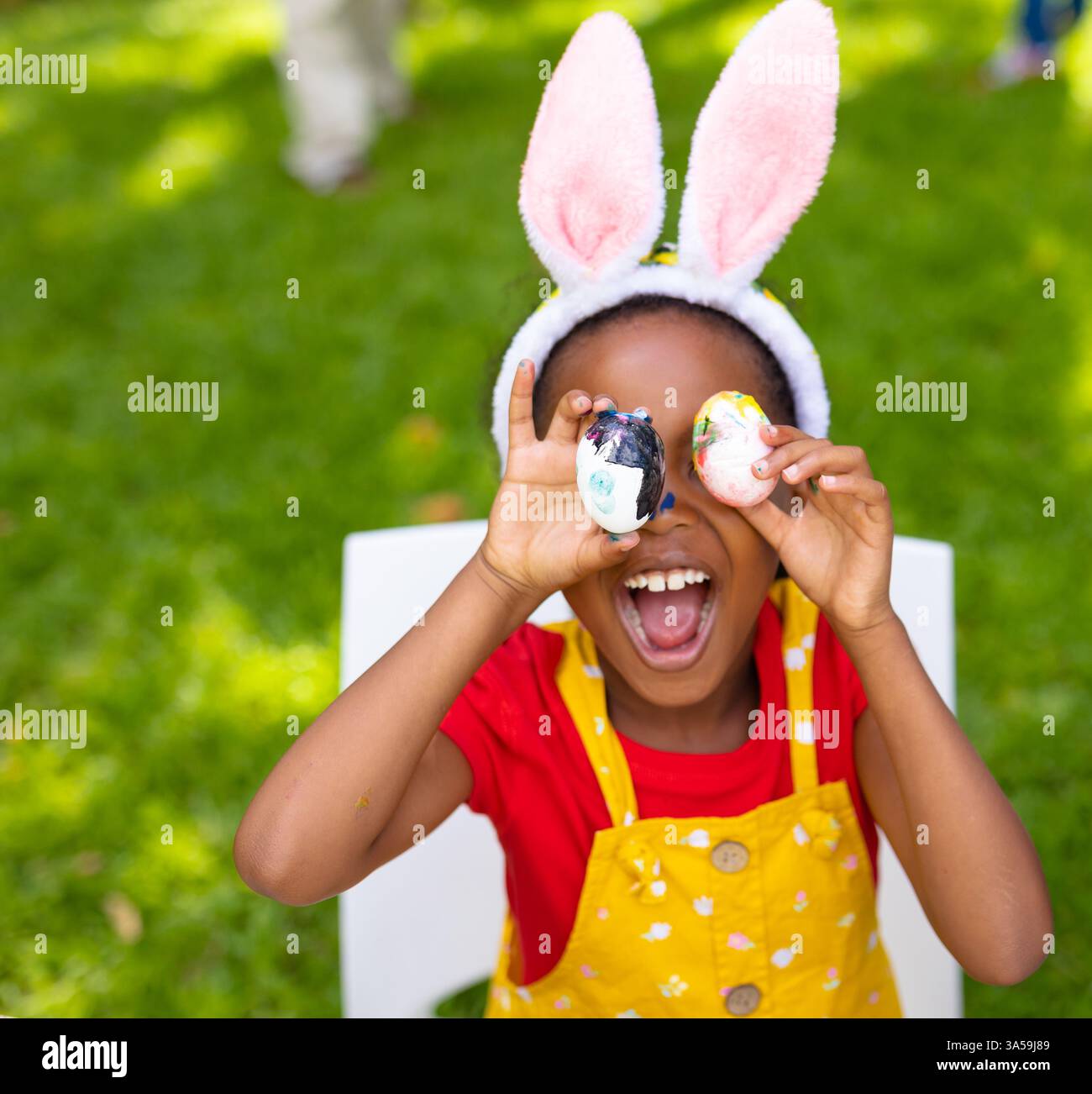 African American girl wearing bunny ears holding decorated eggs ...
