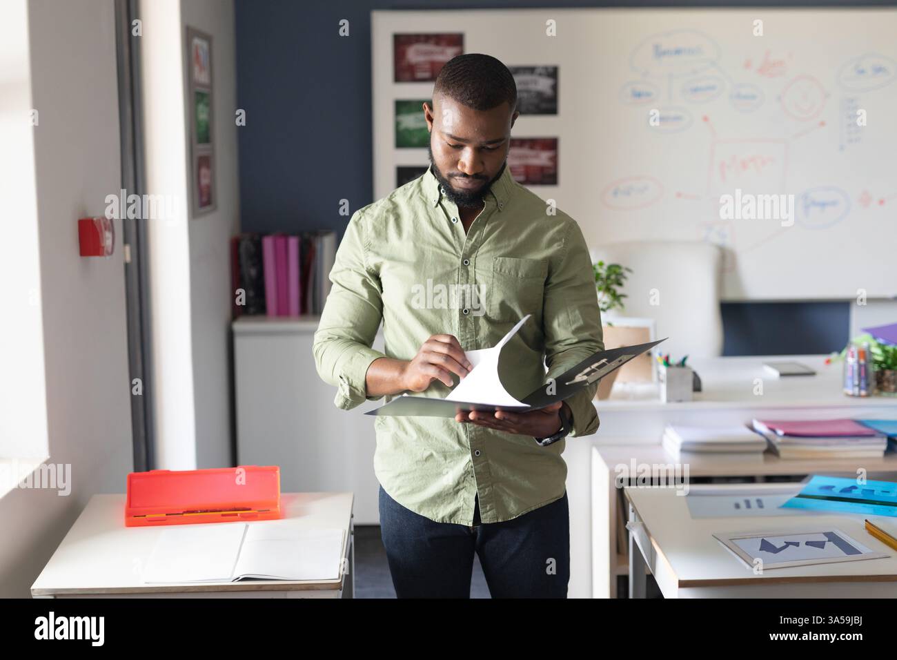 In school, focused man reviewing documents in modern classroom ...