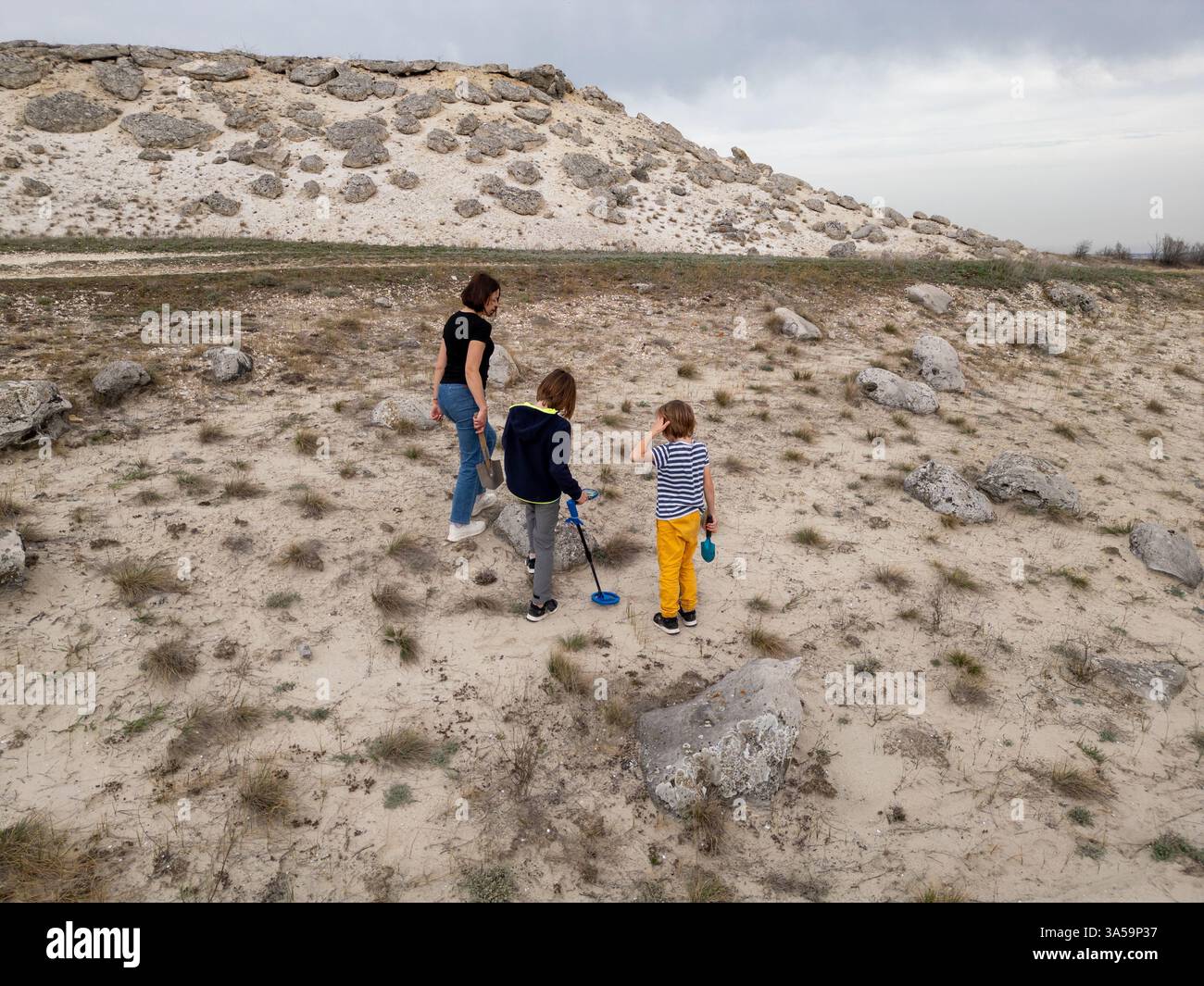 A mother and her two sons searching for treasures in a sandy outdoor ...