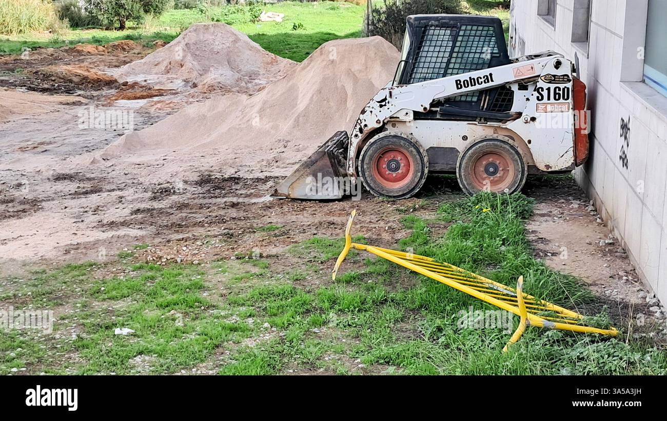 Bobcat s160 skid steer loader parked near a pile of sand and a fallen ...
