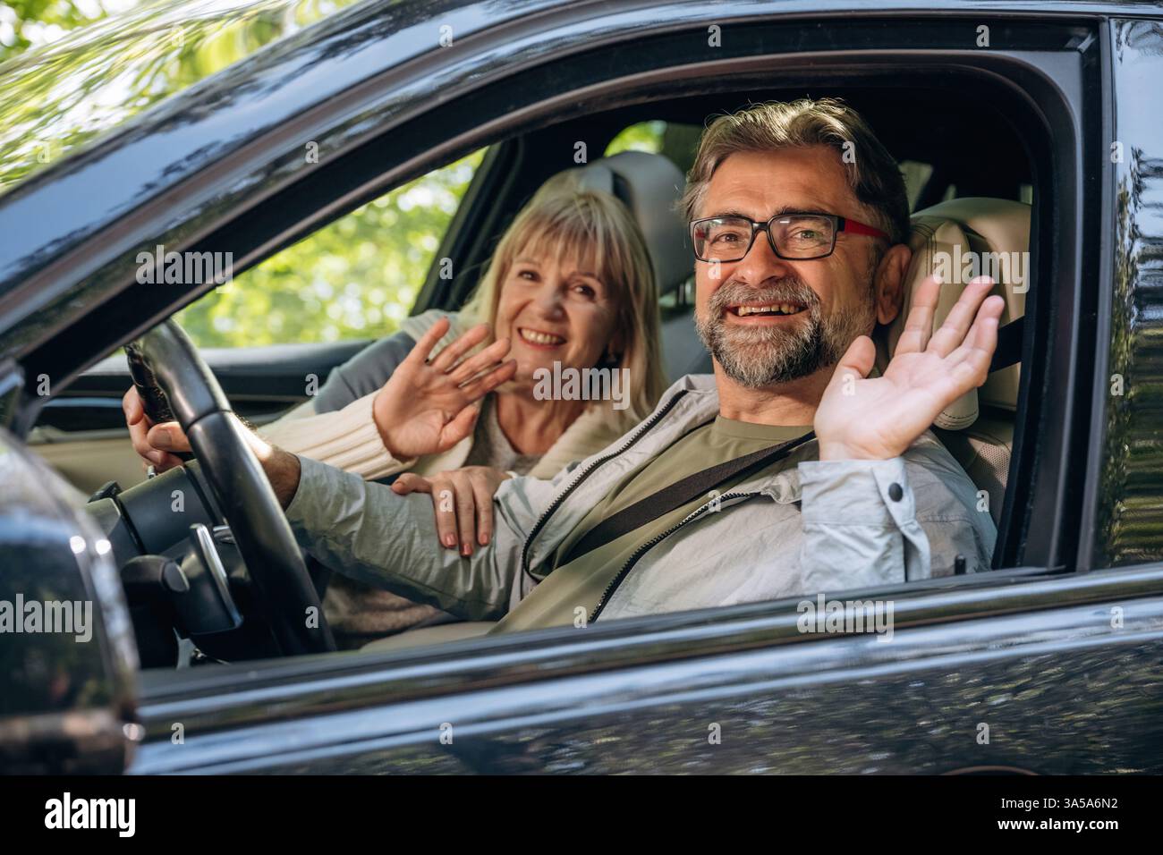 Greetings hands gestures. Senior couple driving in the modern car at ...