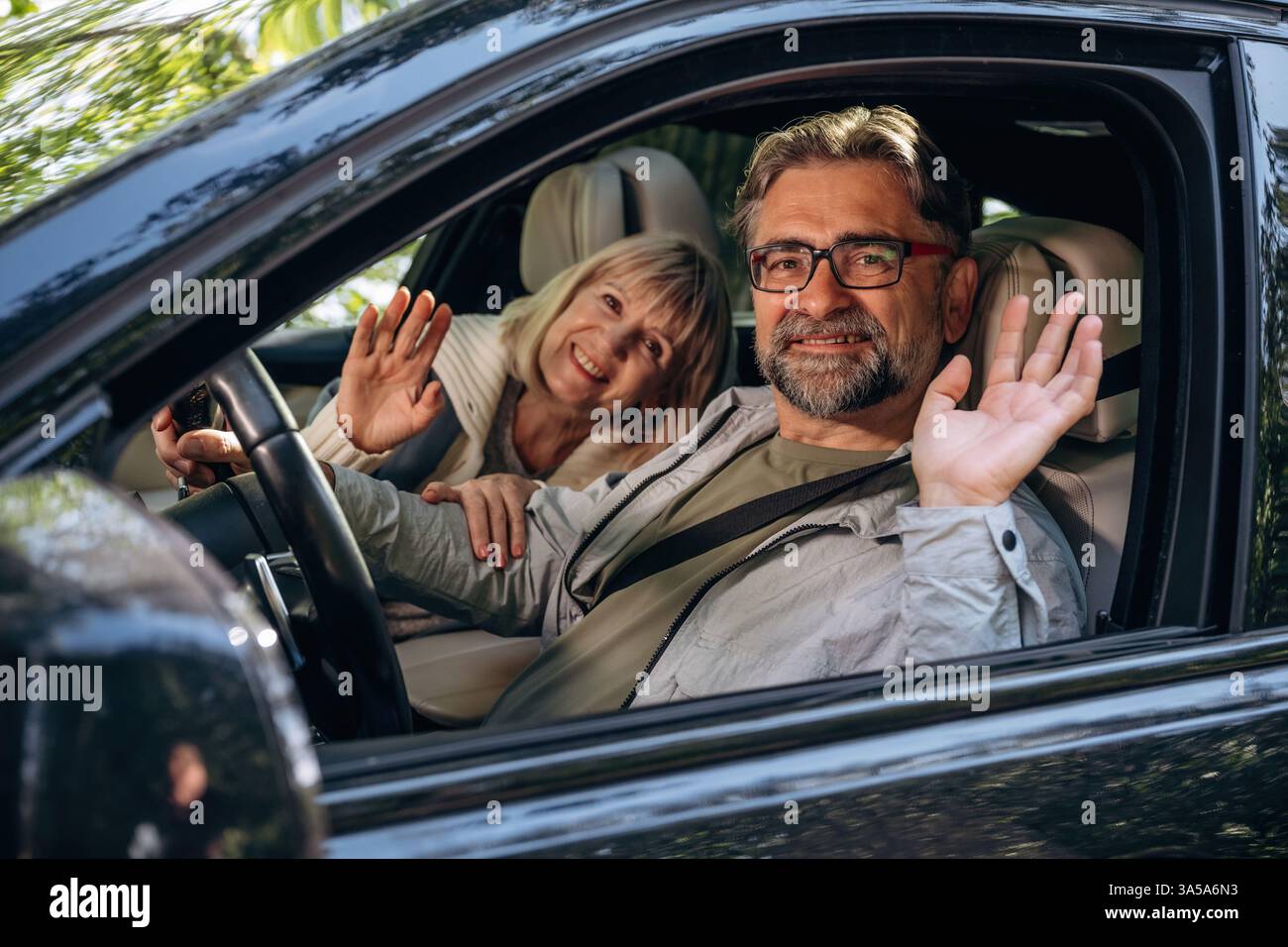 Greetings hands gestures. Senior couple driving in the modern car at ...