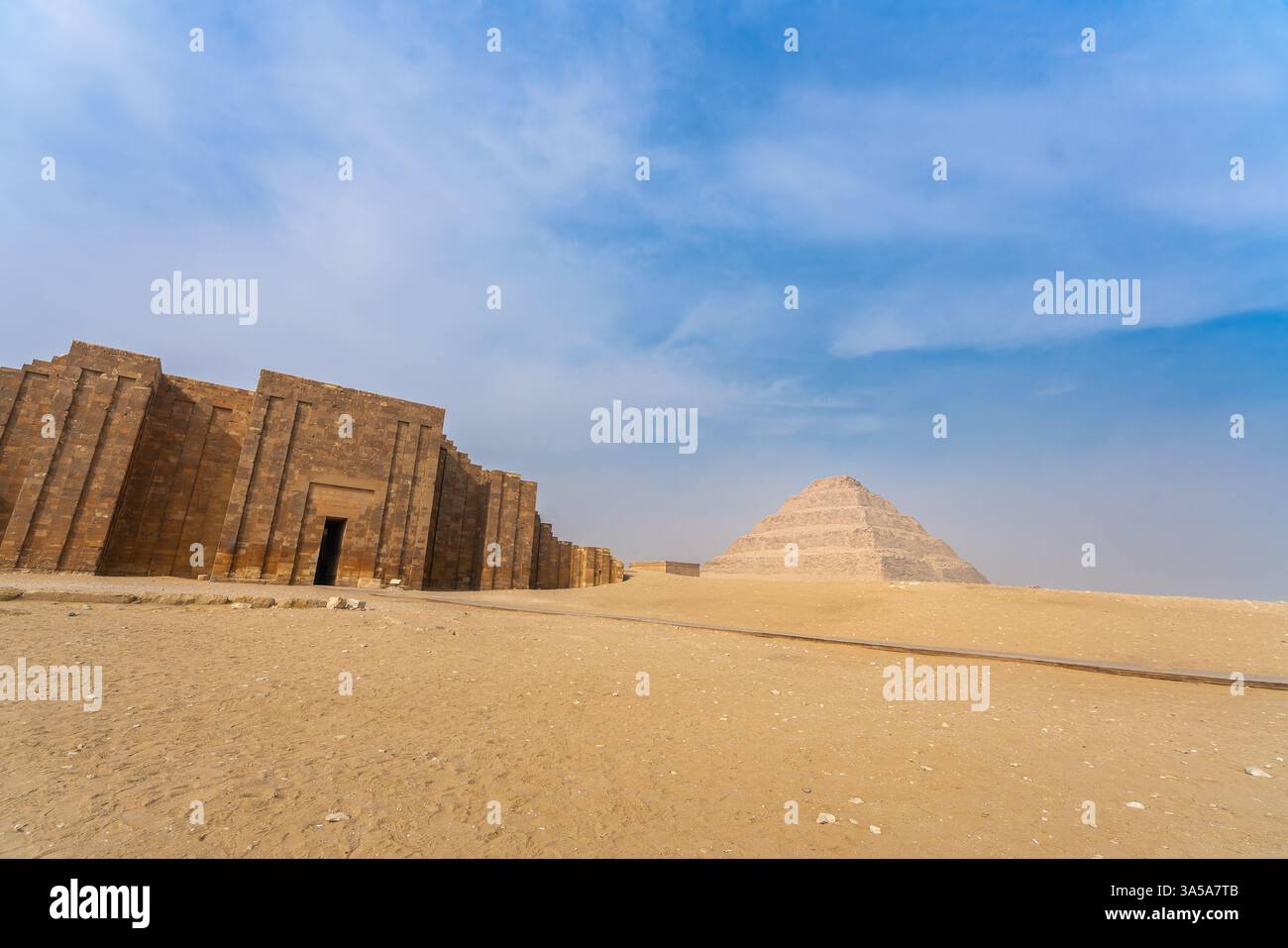 A beige Step Pyramid of Zoser rises in a sandy desert under a clear ...