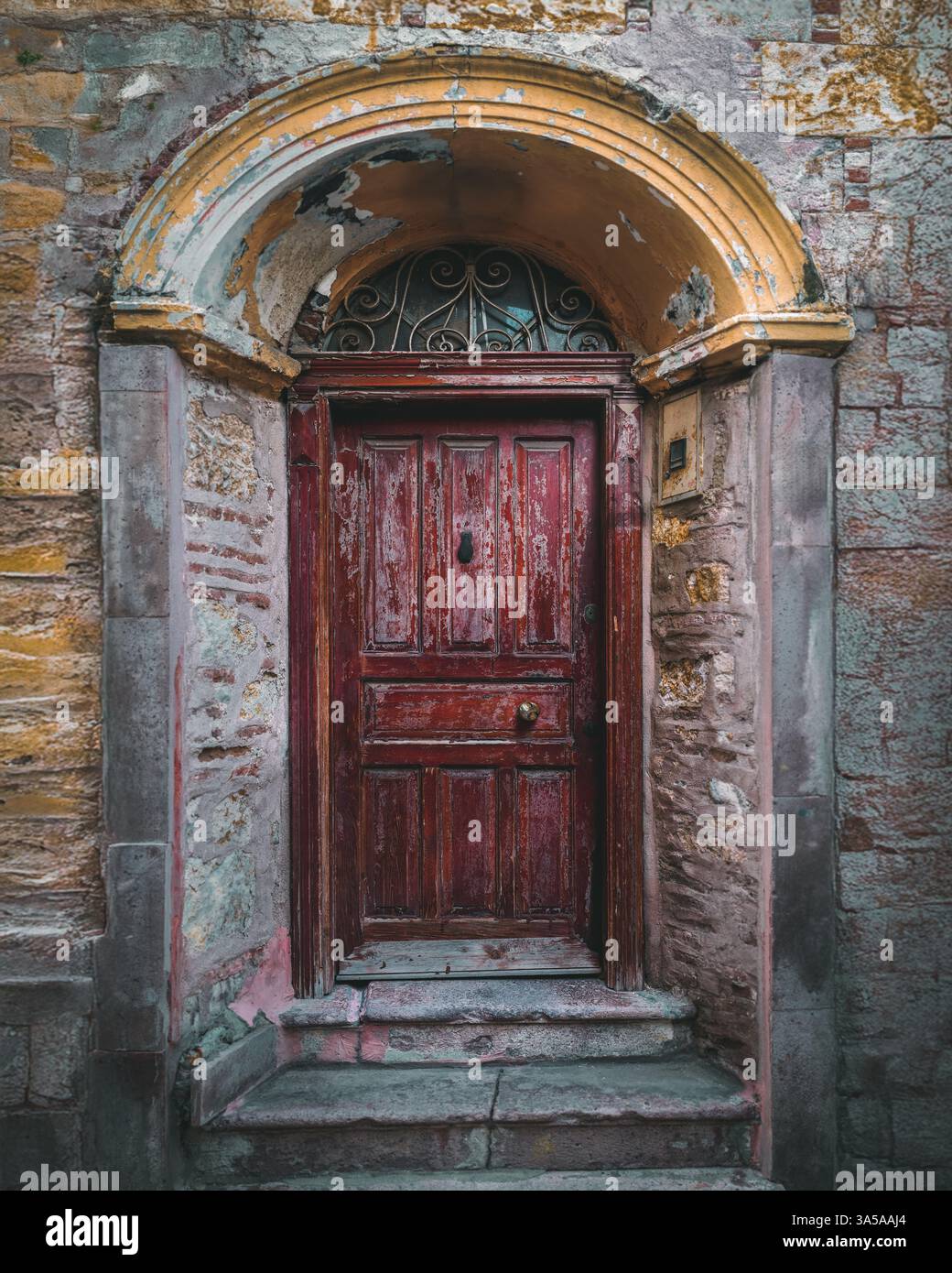 Dark red wooden door with worn paint and iron knocker, set in a yellow ...