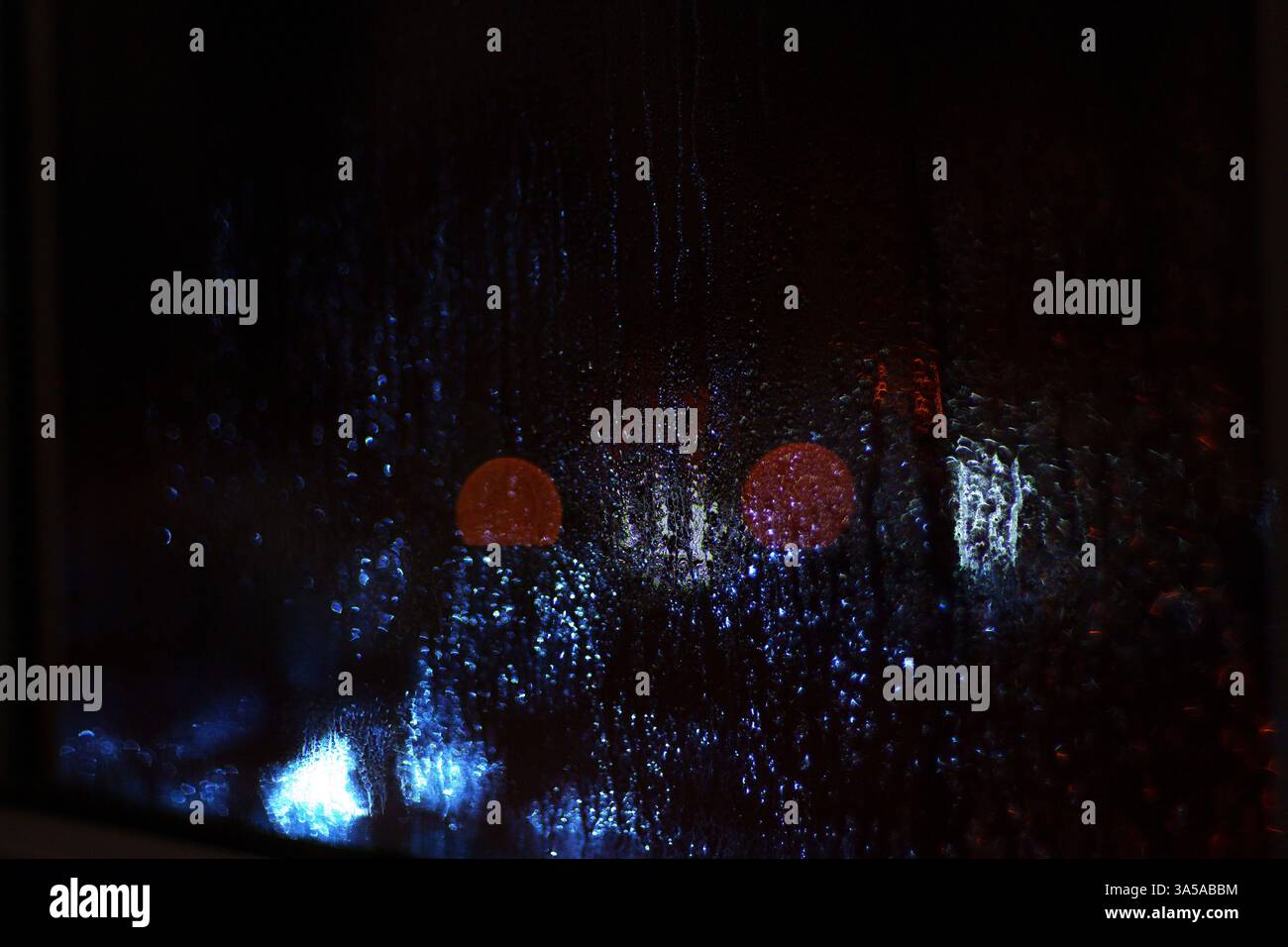 Softly illuminated colors bleed through a rain-streaked window ...