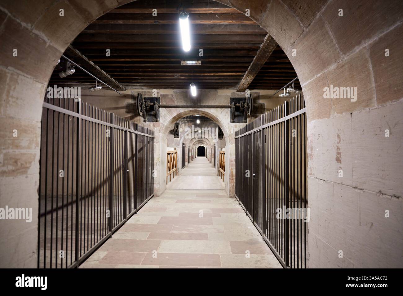 Underground corridor in Strasbourg featuring stone arches, metal gates ...