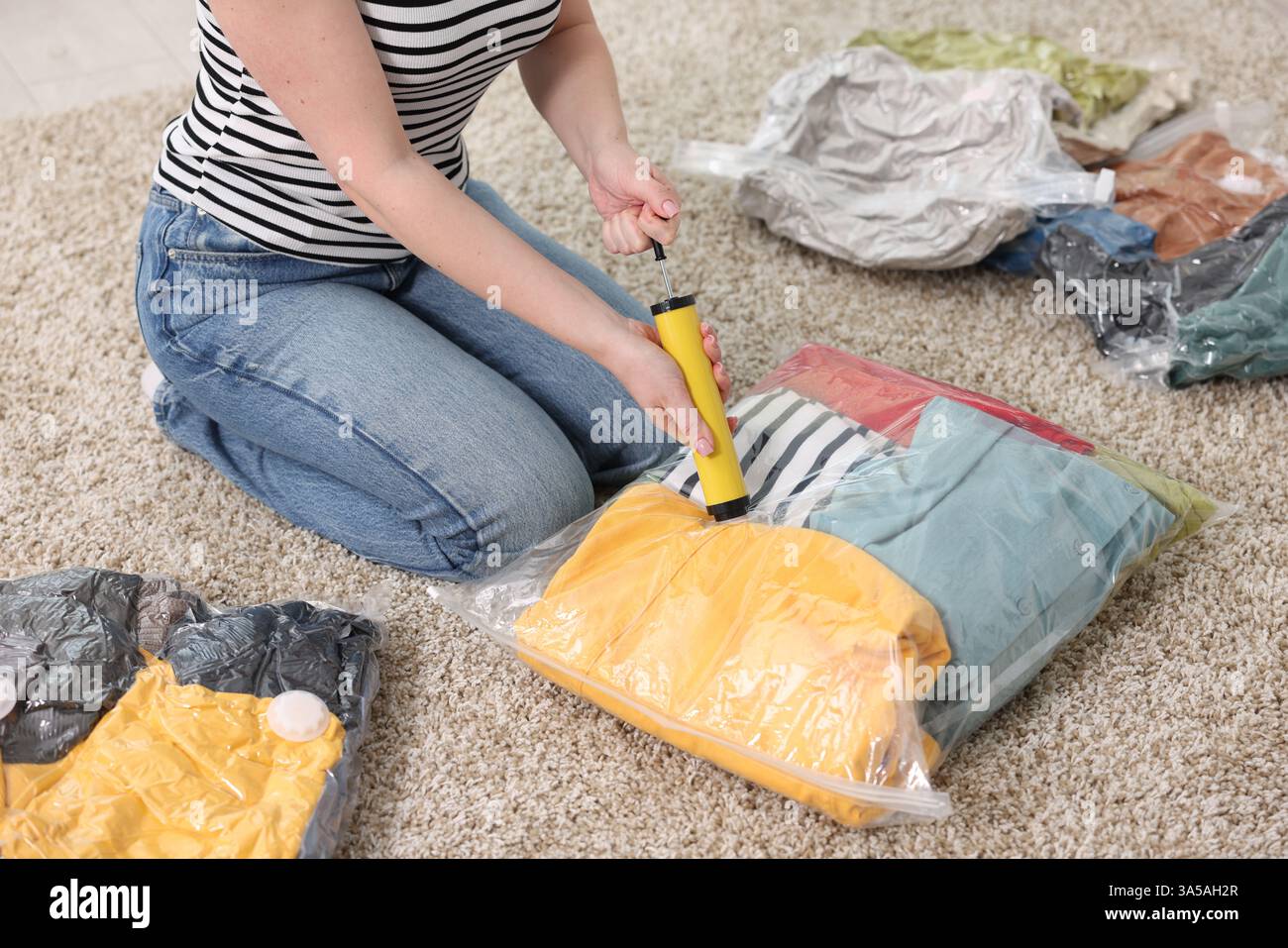 Woman sealing vacuum bag with clothes on floor at home, closeup Stock ...