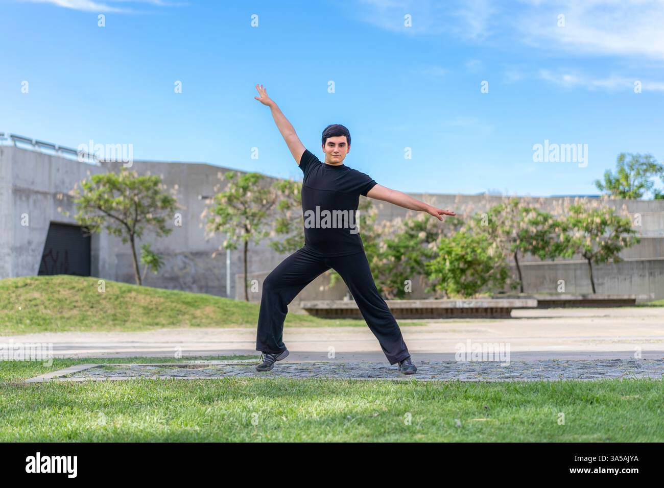 Dynamic young man striking a pose with outstretched arms in a park ...