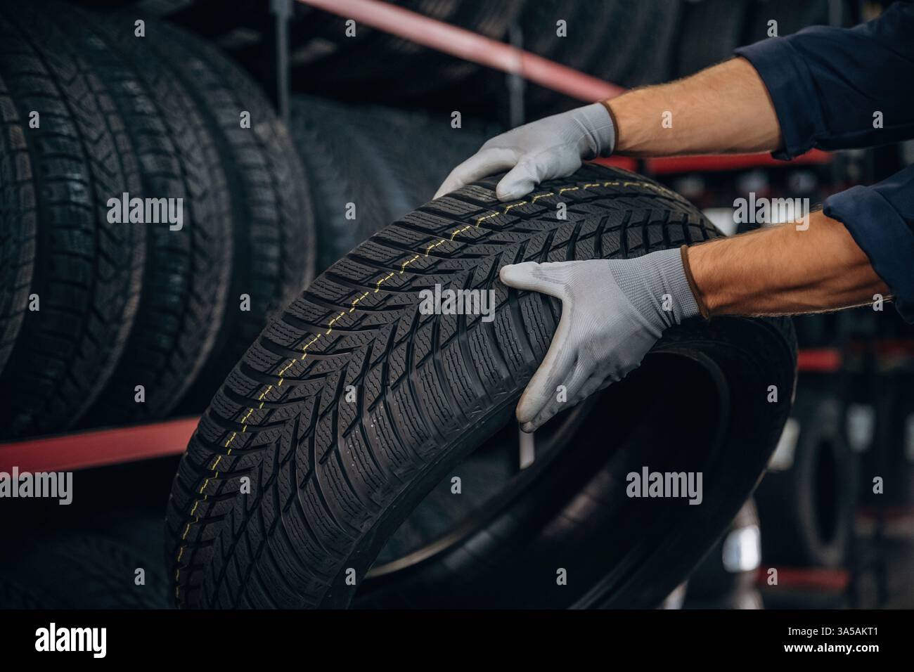In grey gloves, taking the tire. Man worker is maintenance station with ...
