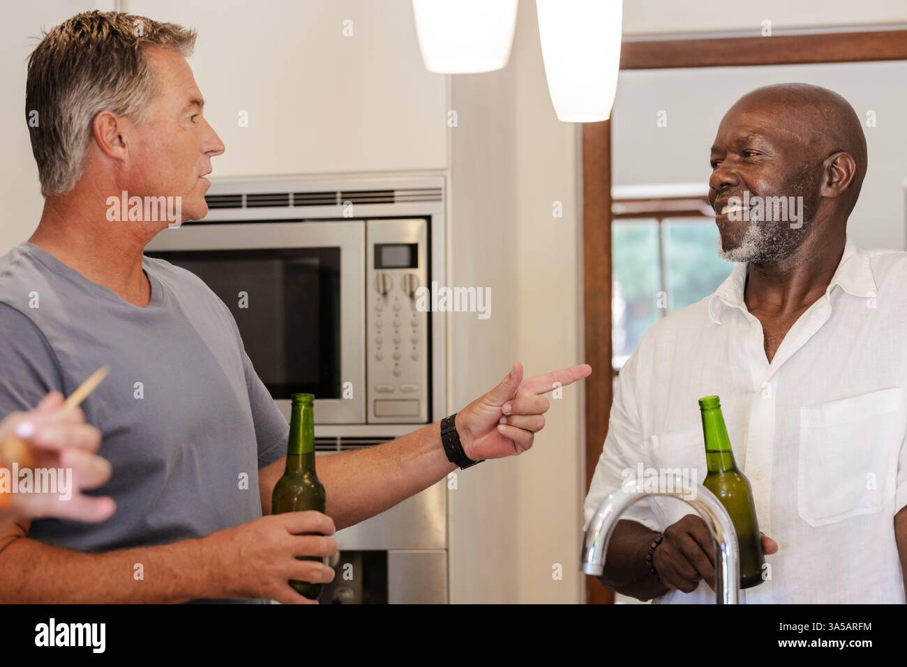 Two senior men enjoying conversation and drinks in modern kitchen ...