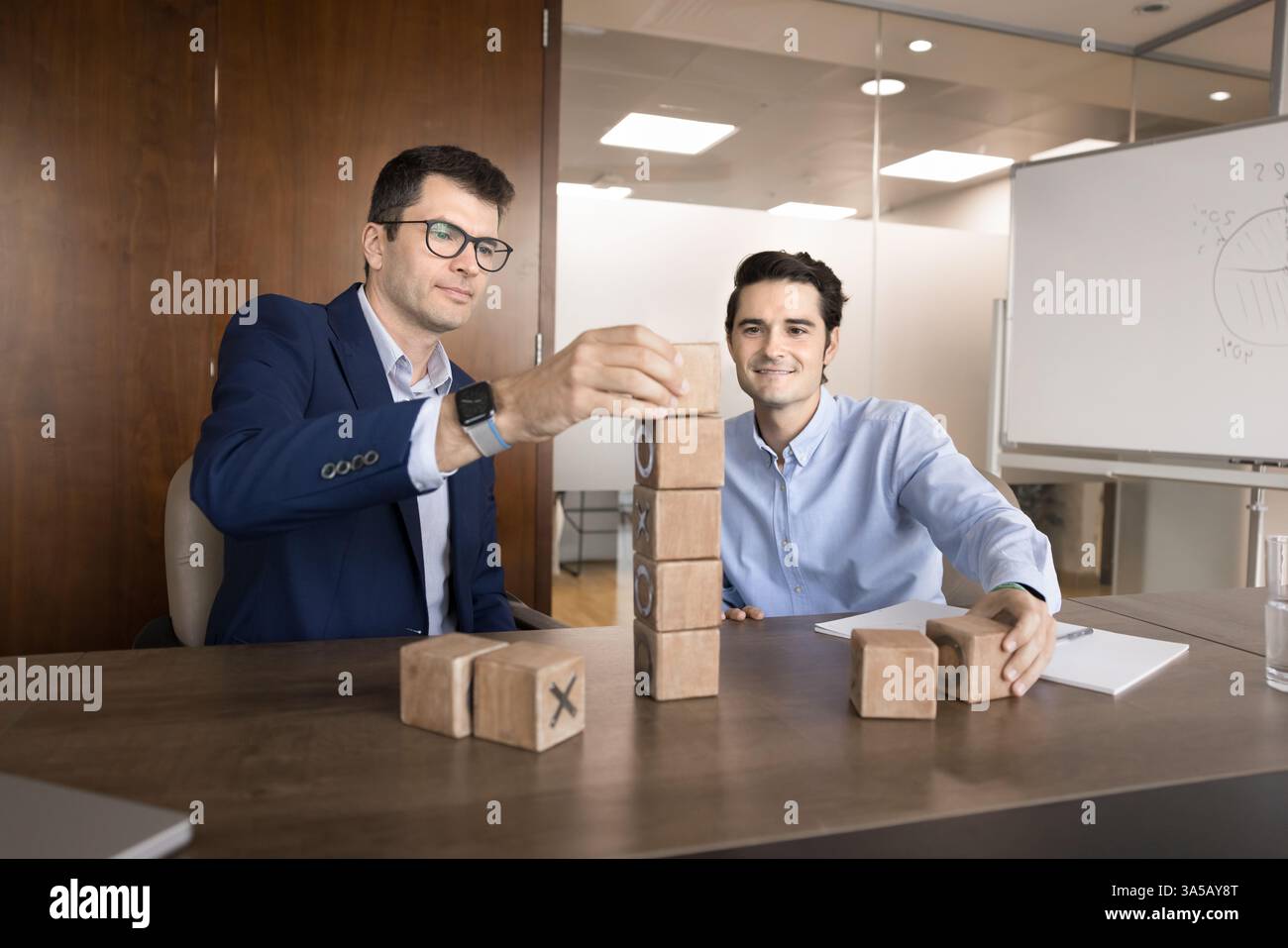 Two businessmen build tower from wooden blocks Stock Photo - Alamy