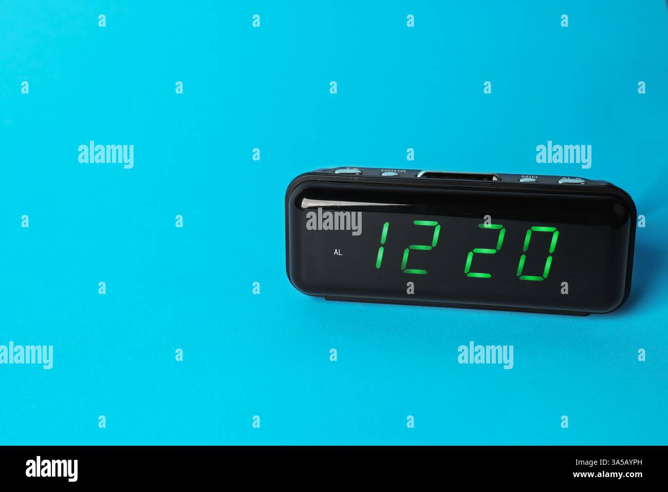 Digital alarm clock showing 12:20 o'clock on light blue background ...
