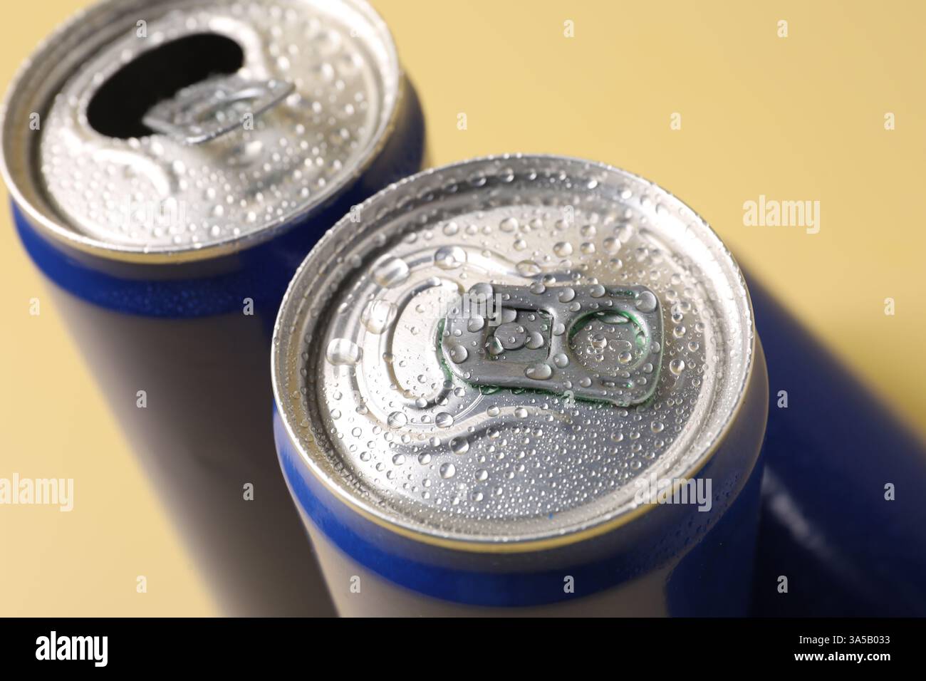 Blue aluminium cans of beverage on pale yellow background, closeup ...