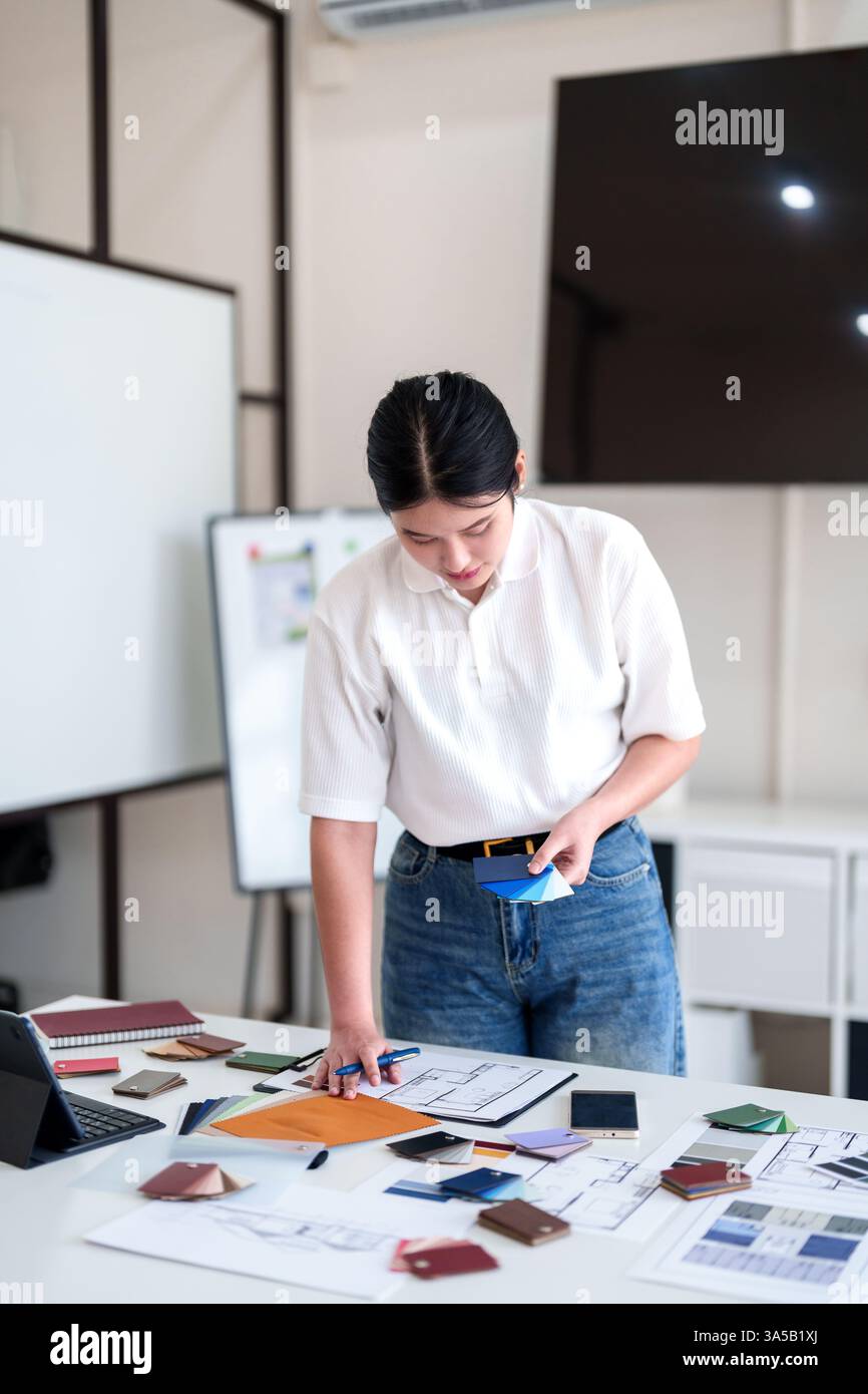 Young architect selecting materials and color swatches while standing at modern interior design ...