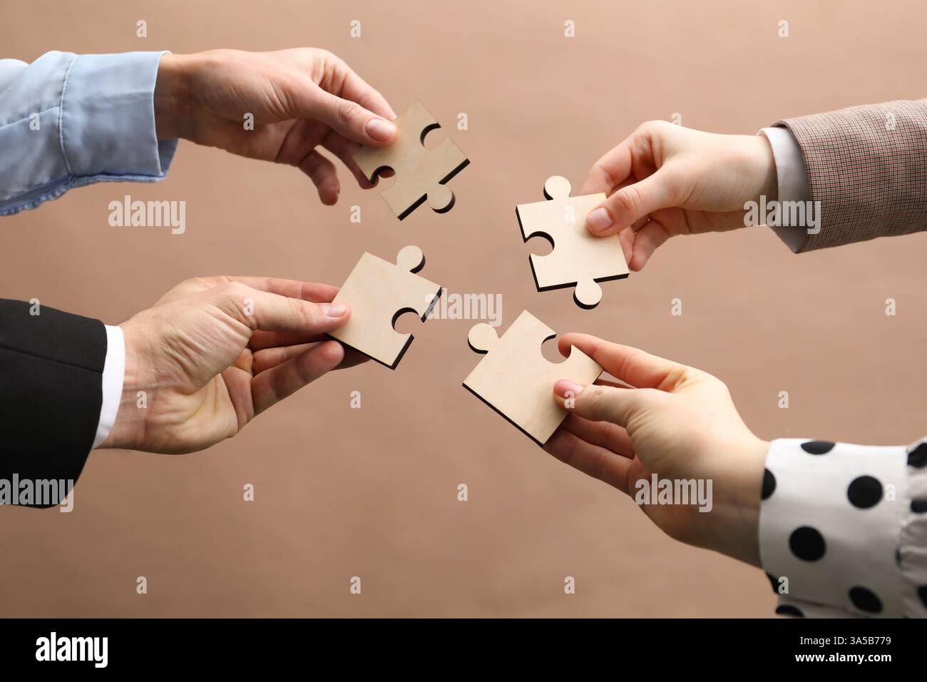Teamwork. Group of people putting puzzle pieces together on beige background, closeup Stock ...