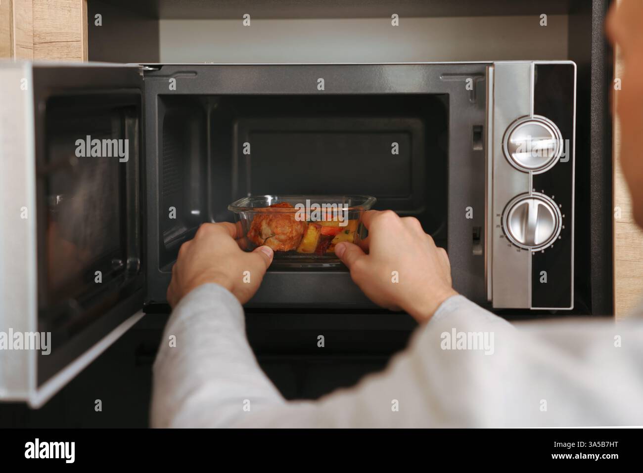 Man putting container with lunch into microwave in kitchen, closeup ...