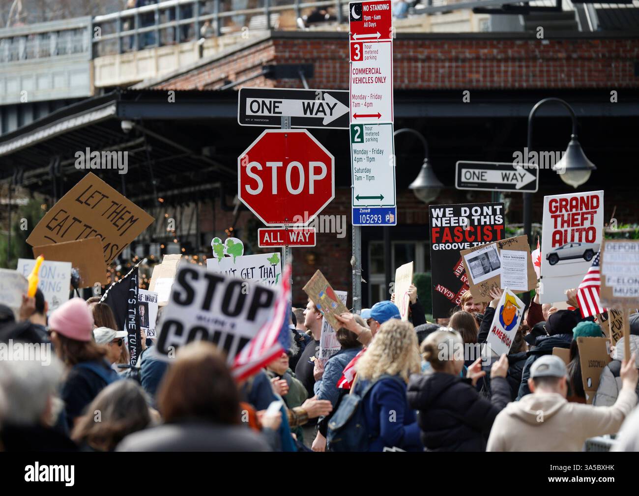Protesters hold signs when they gather outside of the Tesla dealership ...