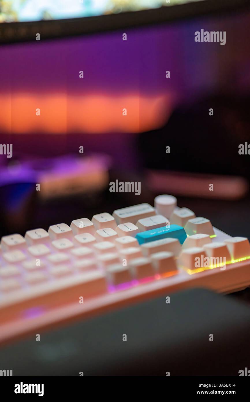 Close-up of a white keyboard with a blue "enter" key, illuminated by colorful lights, in front ...
