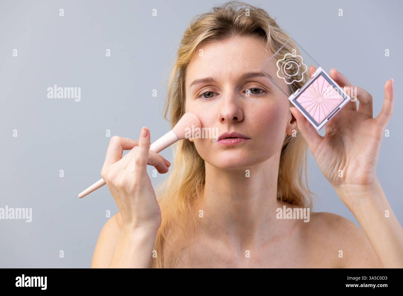 A Young Woman Applying Makeup with Brush and Holding Blush Compact for ...